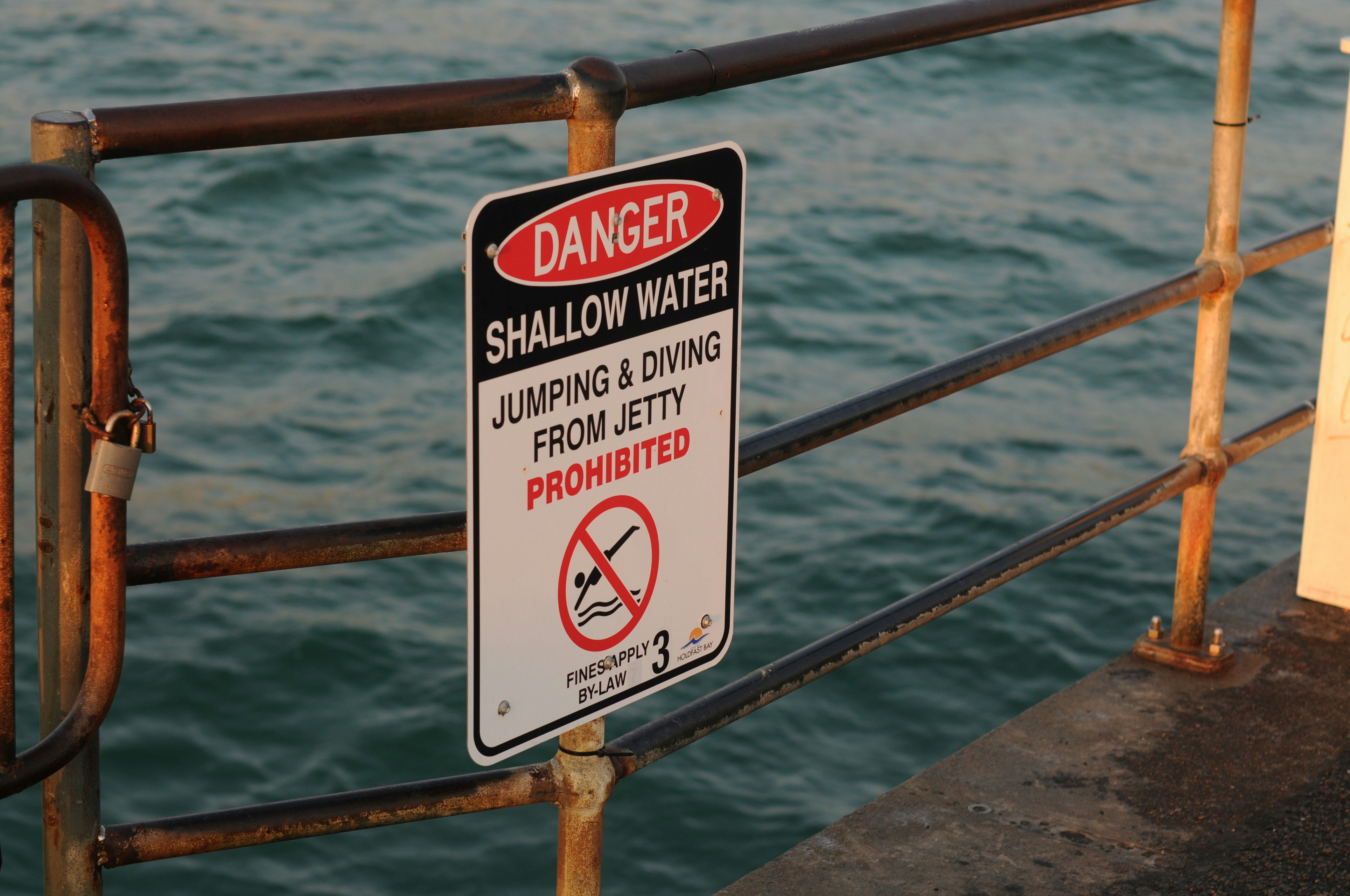 A warning sign on a railing near a body of water photo – Free Sign ...