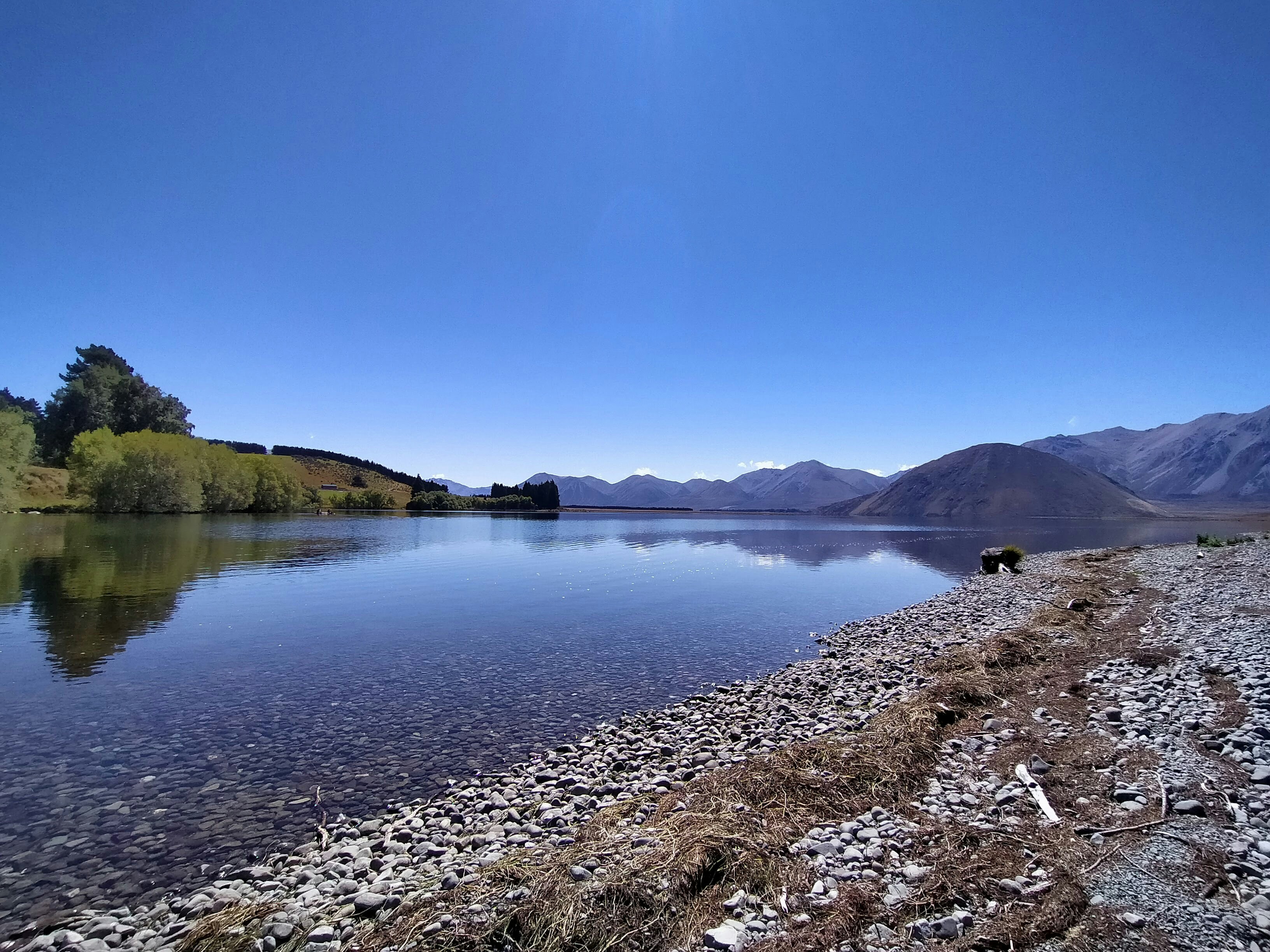 Alpine Mirror: Pebble Beach Framing a Calm Lake and Snowy Peaks