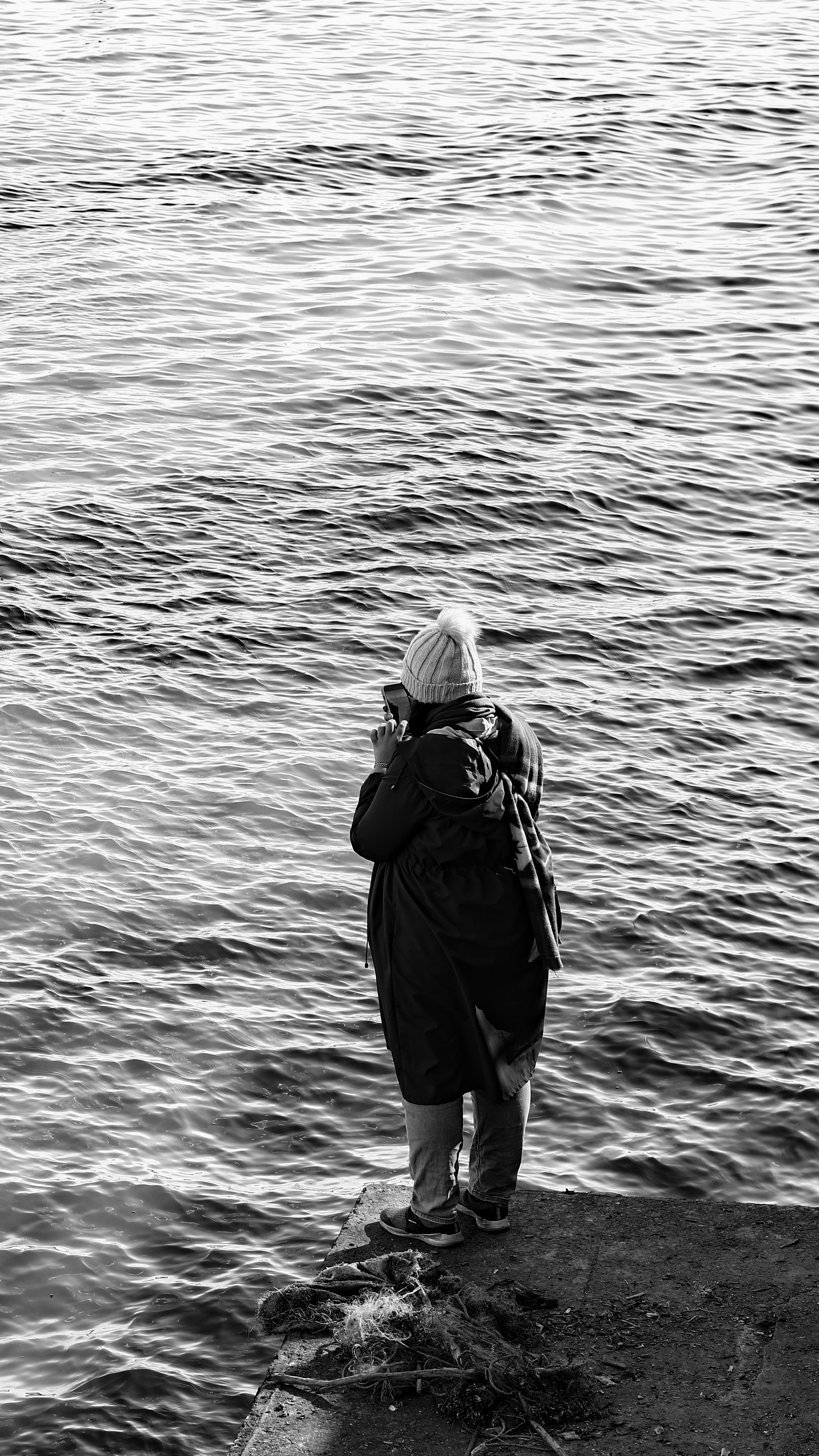 Person standing on the edge of a pier, gazing thoughtfully at the rippling water. The scene captures a moment of solitude and reflection.