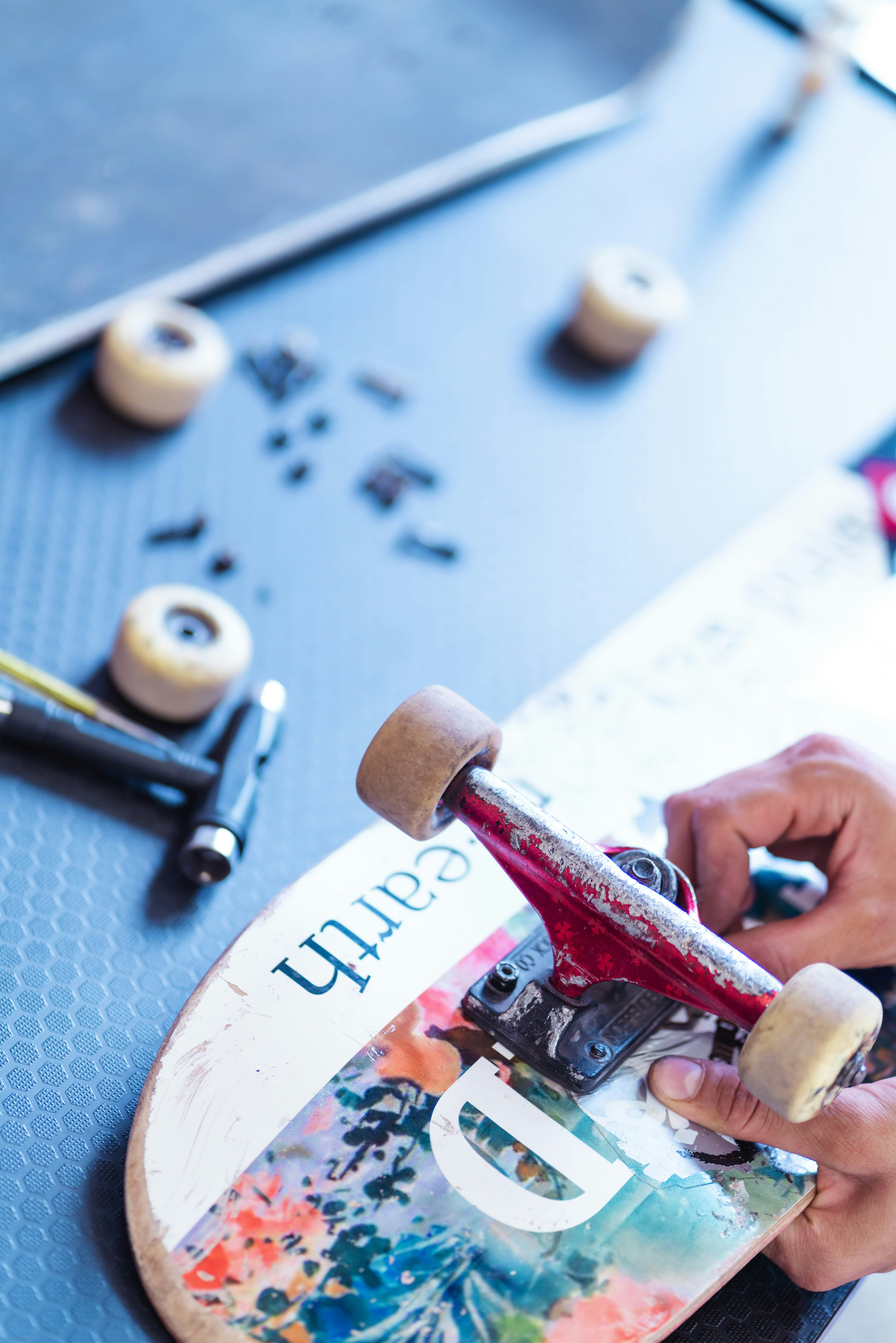 Tightening the Ride: Hands Assemble a Colorful Skateboard on a Blue Workbench