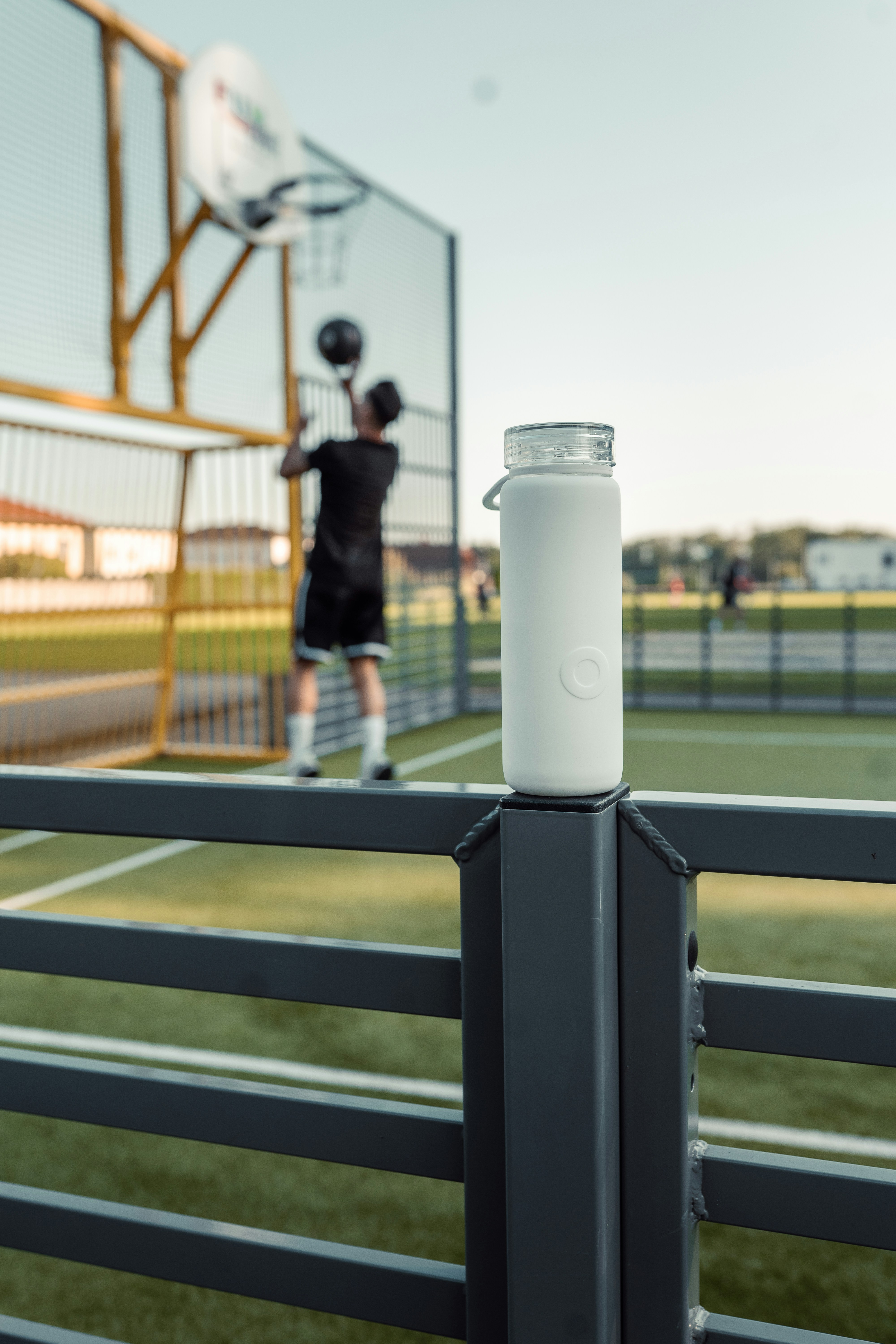 Hydration on the Railing: A Bottle Framing a Quiet Basketball Court