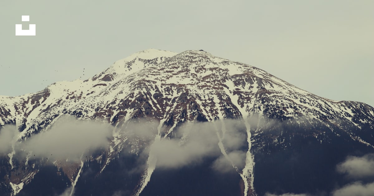 Une Montagne Couverte De Neige Et De Nuages Sous Un Ciel Bleu Photo