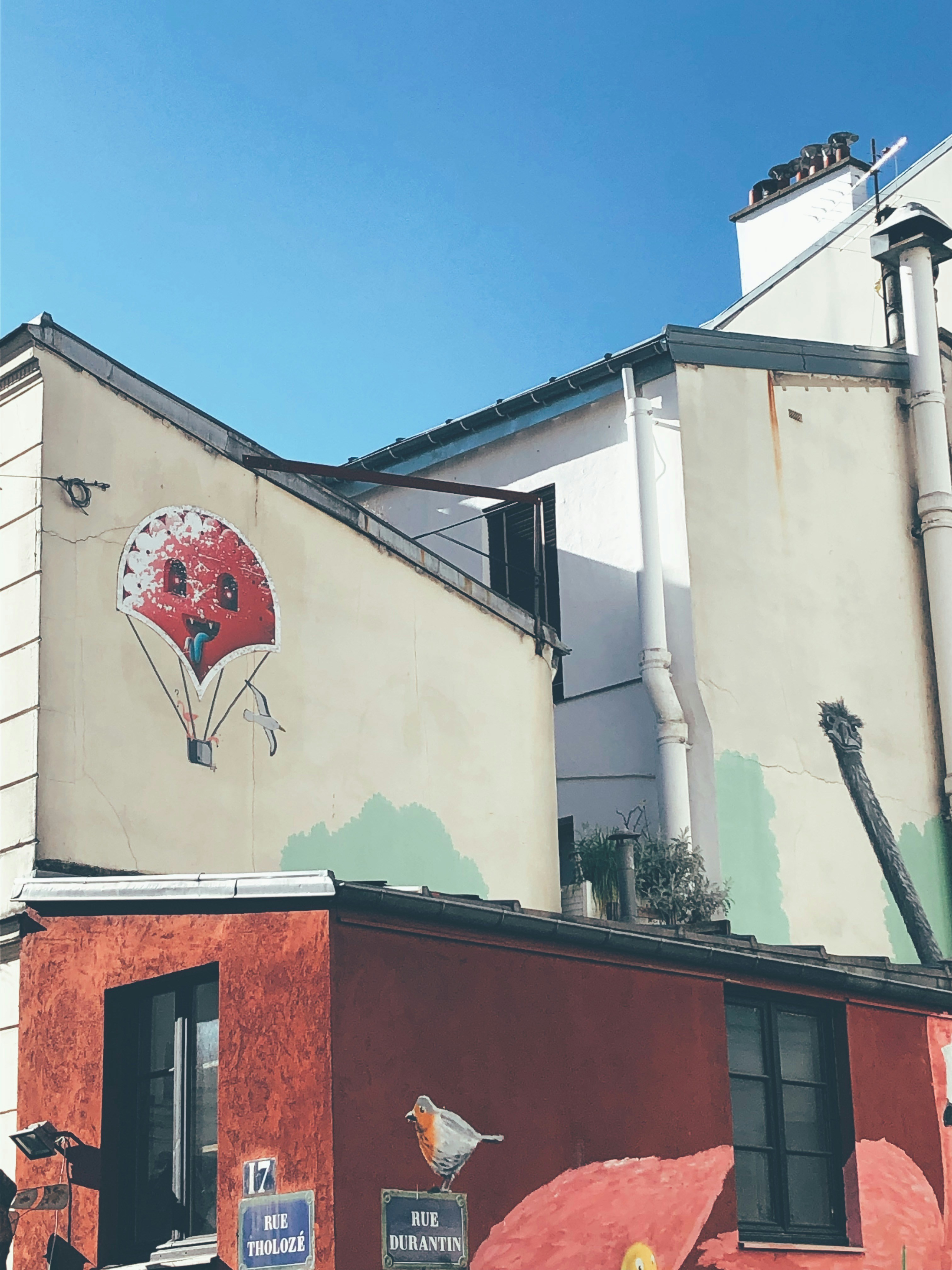 Colorful mural featuring a whimsical hot air balloon and a bird on a vibrant red wall. The playful design adds charm to the urban landscape.