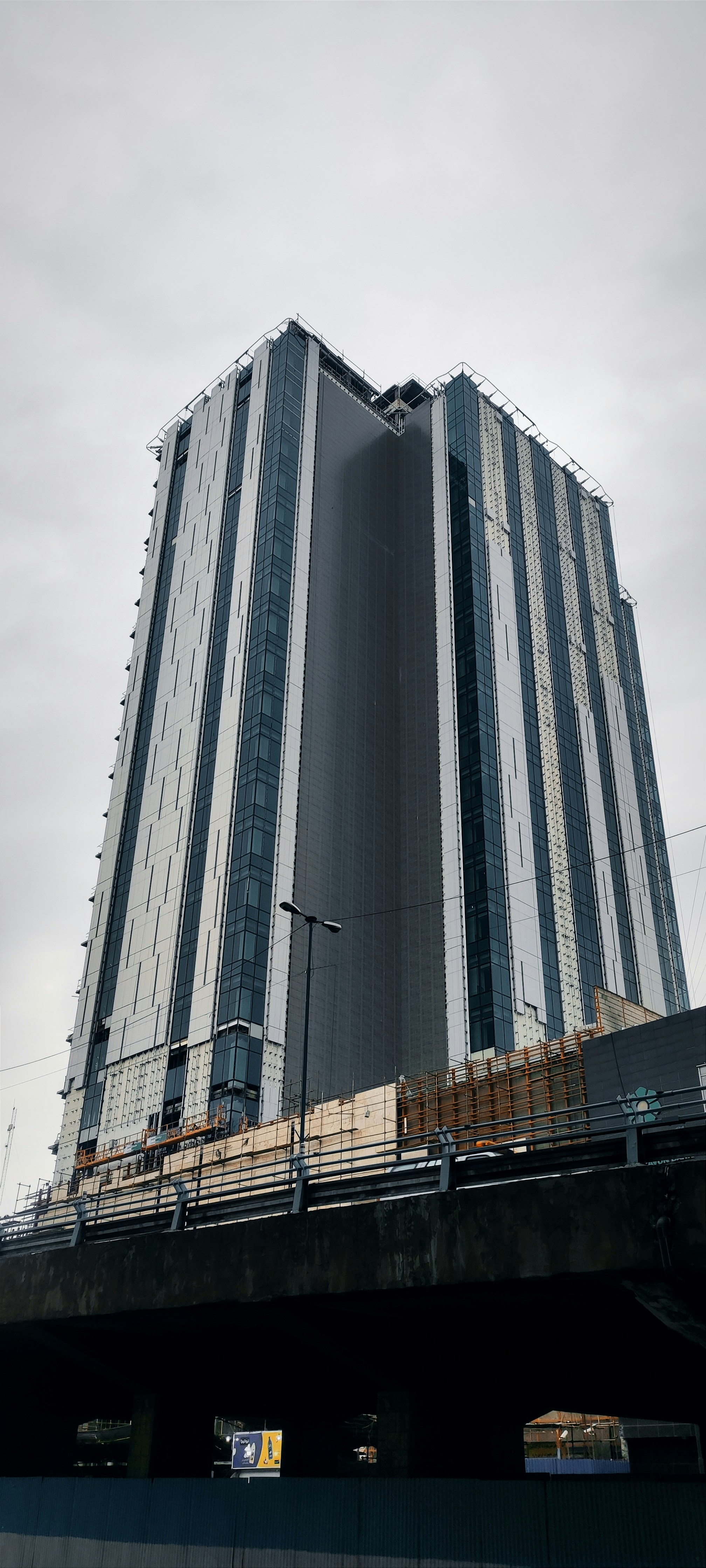 A towering skyscraper under construction, showcasing a blend of glass and steel against a cloudy sky.