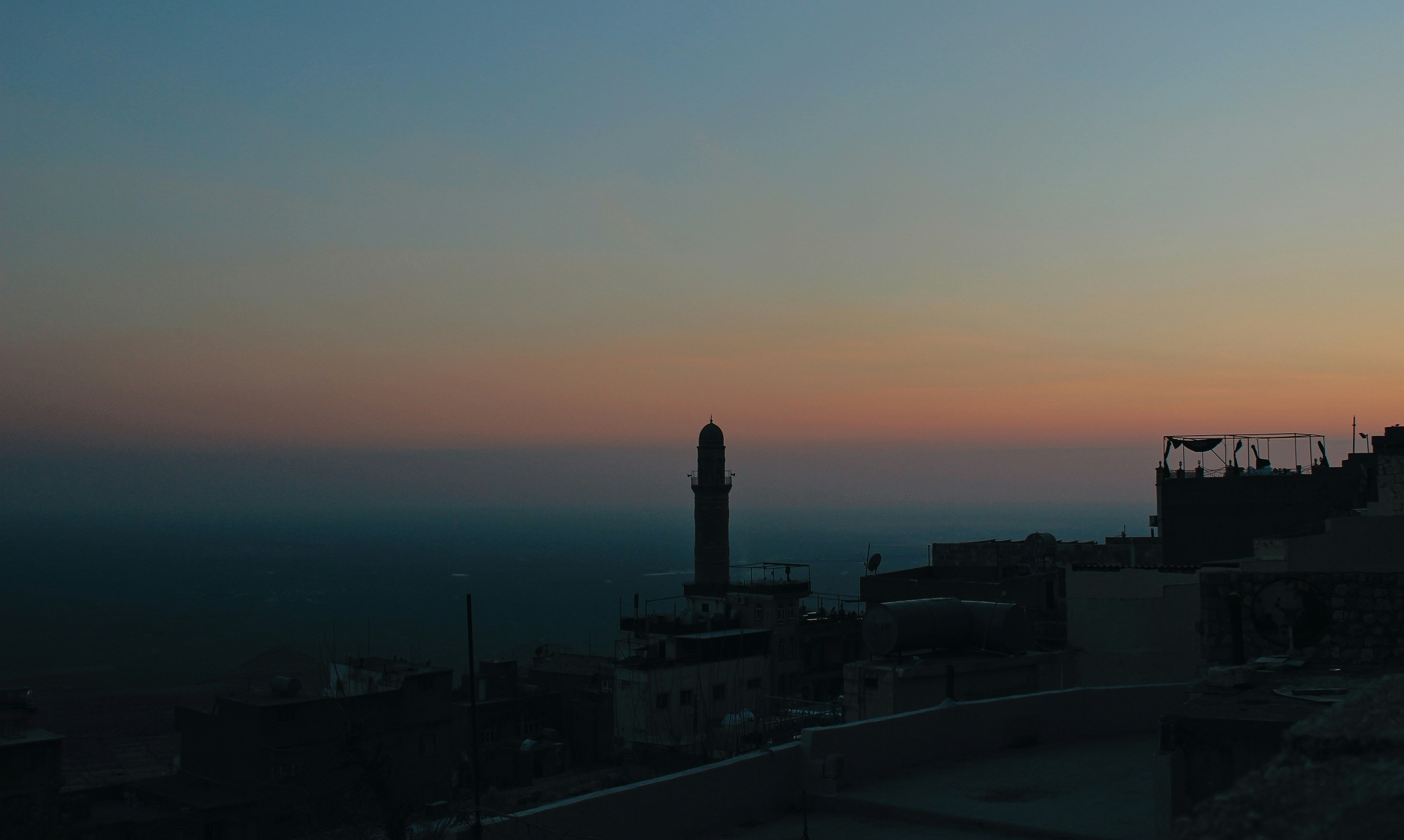 Silhouette of a tower against a gradient sunset sky with buildings in the foreground.