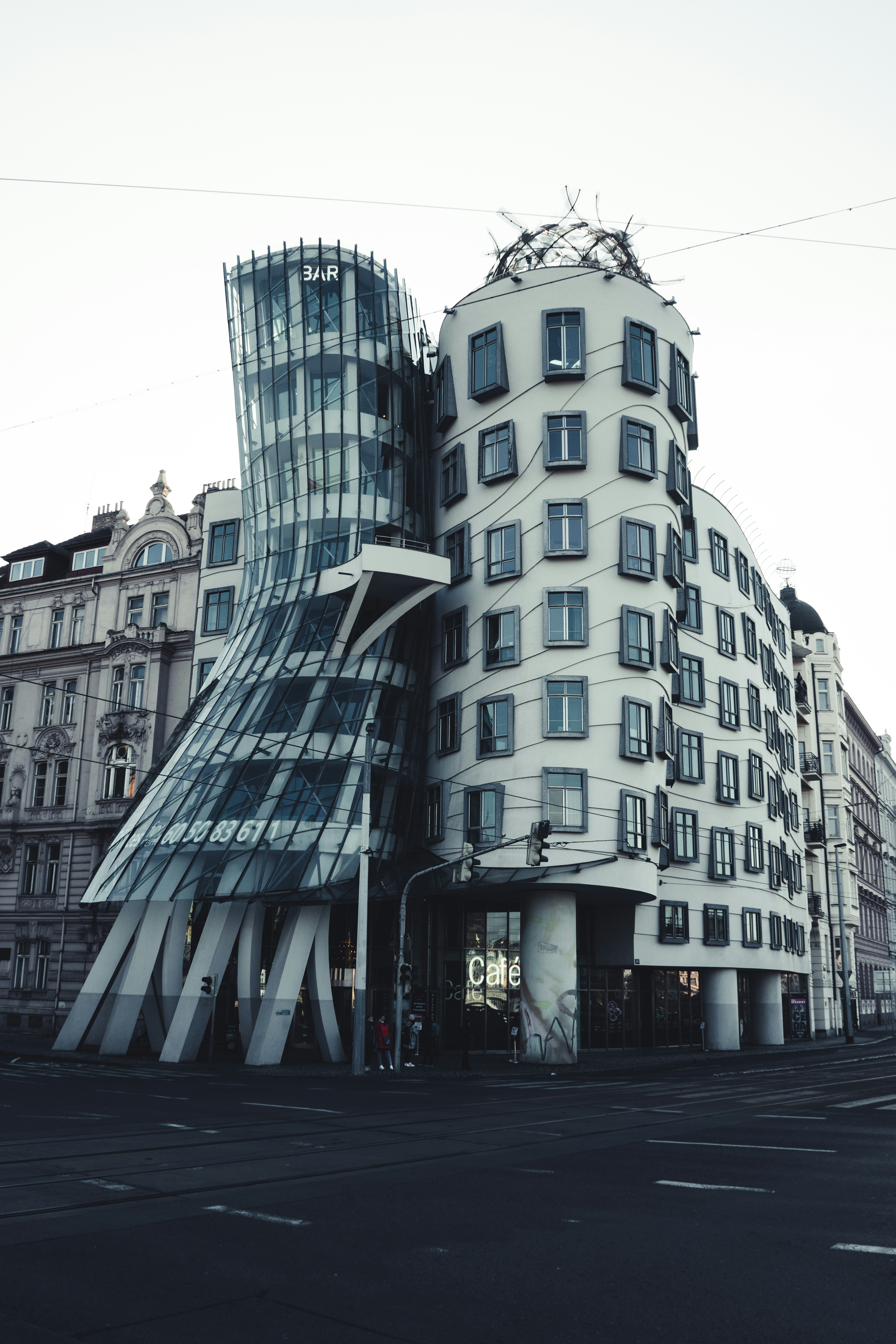 A modern architectural marvel featuring a twisting glass structure juxtaposed with a traditional building, showcasing innovative design elements. The scene captures urban life with pedestrians nearby.