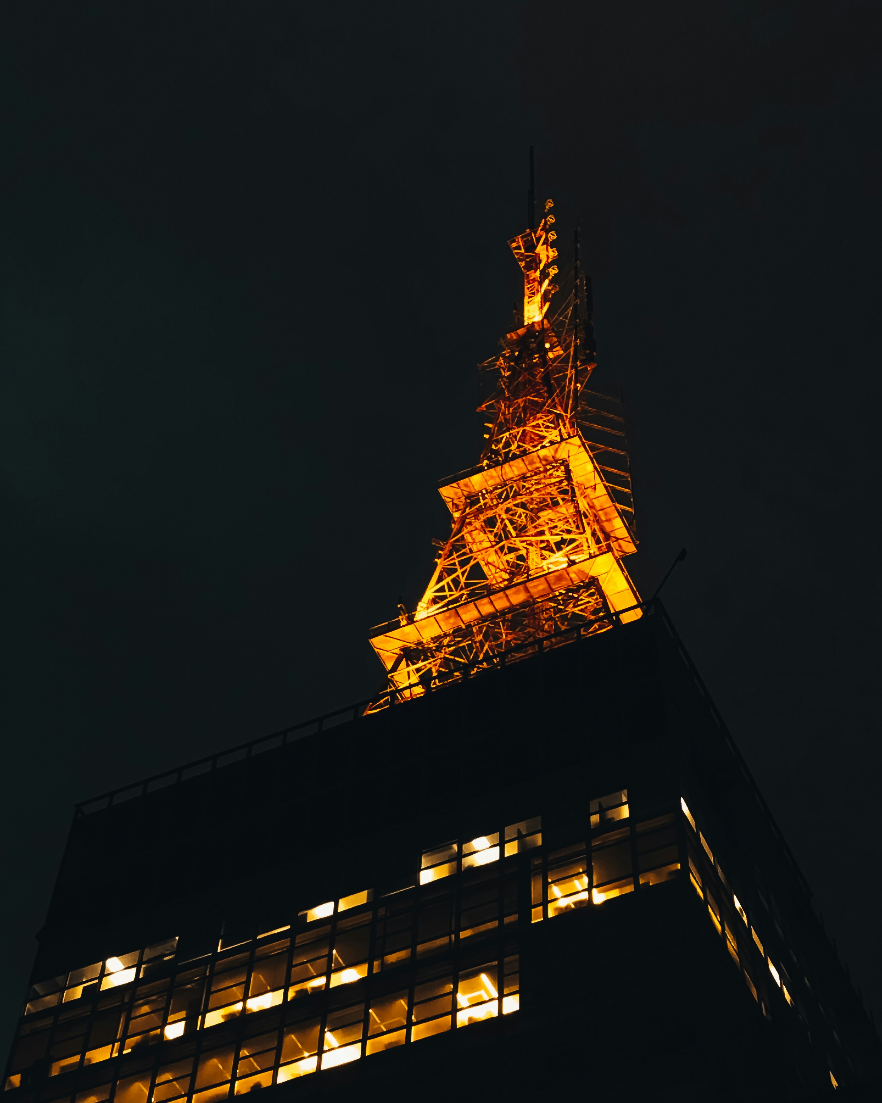 Illuminated tower top glowing with warm light against a dark evening sky.