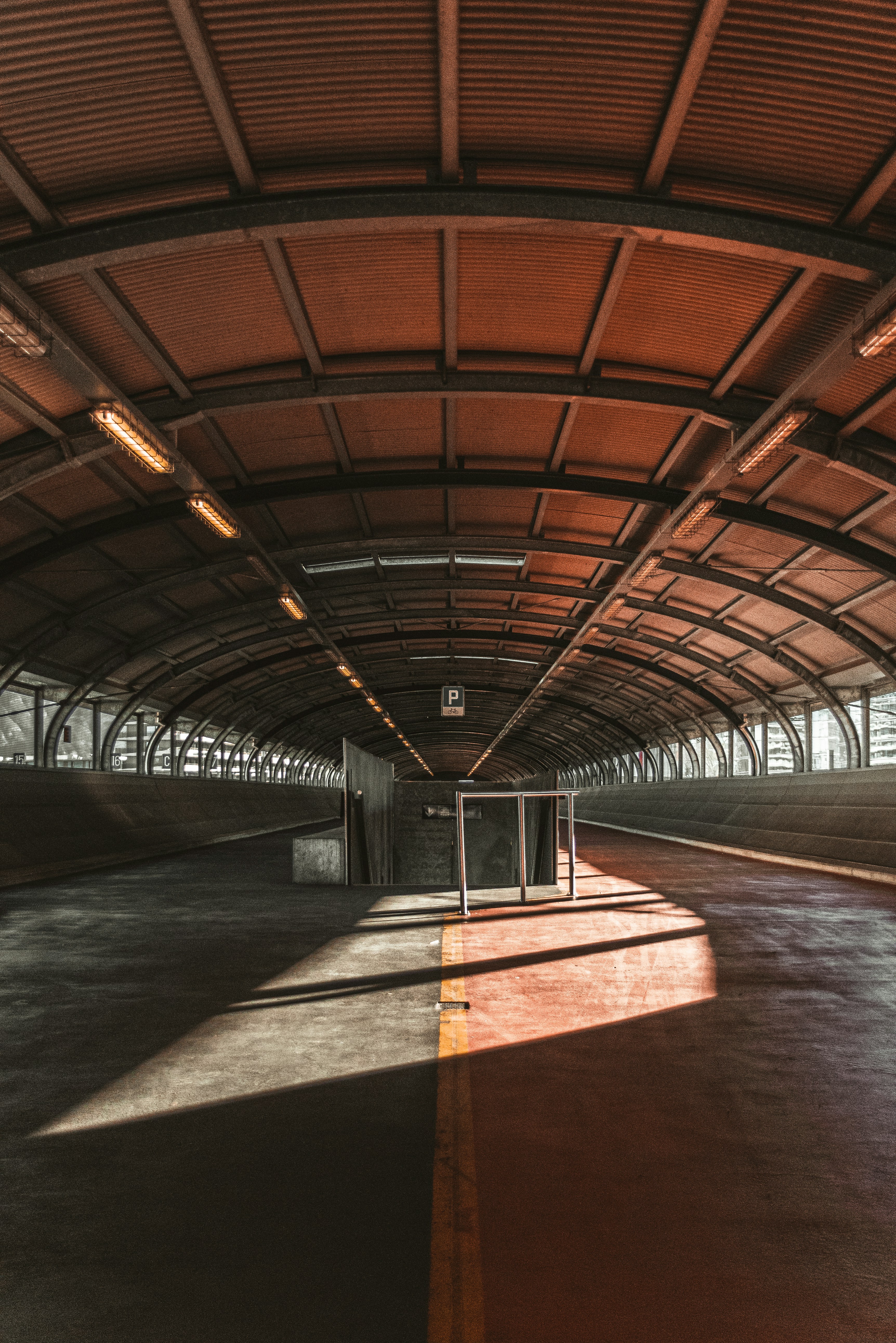 Spacious parking structure with a curved ceiling, illuminated by warm light casting long shadows on the concrete floor.