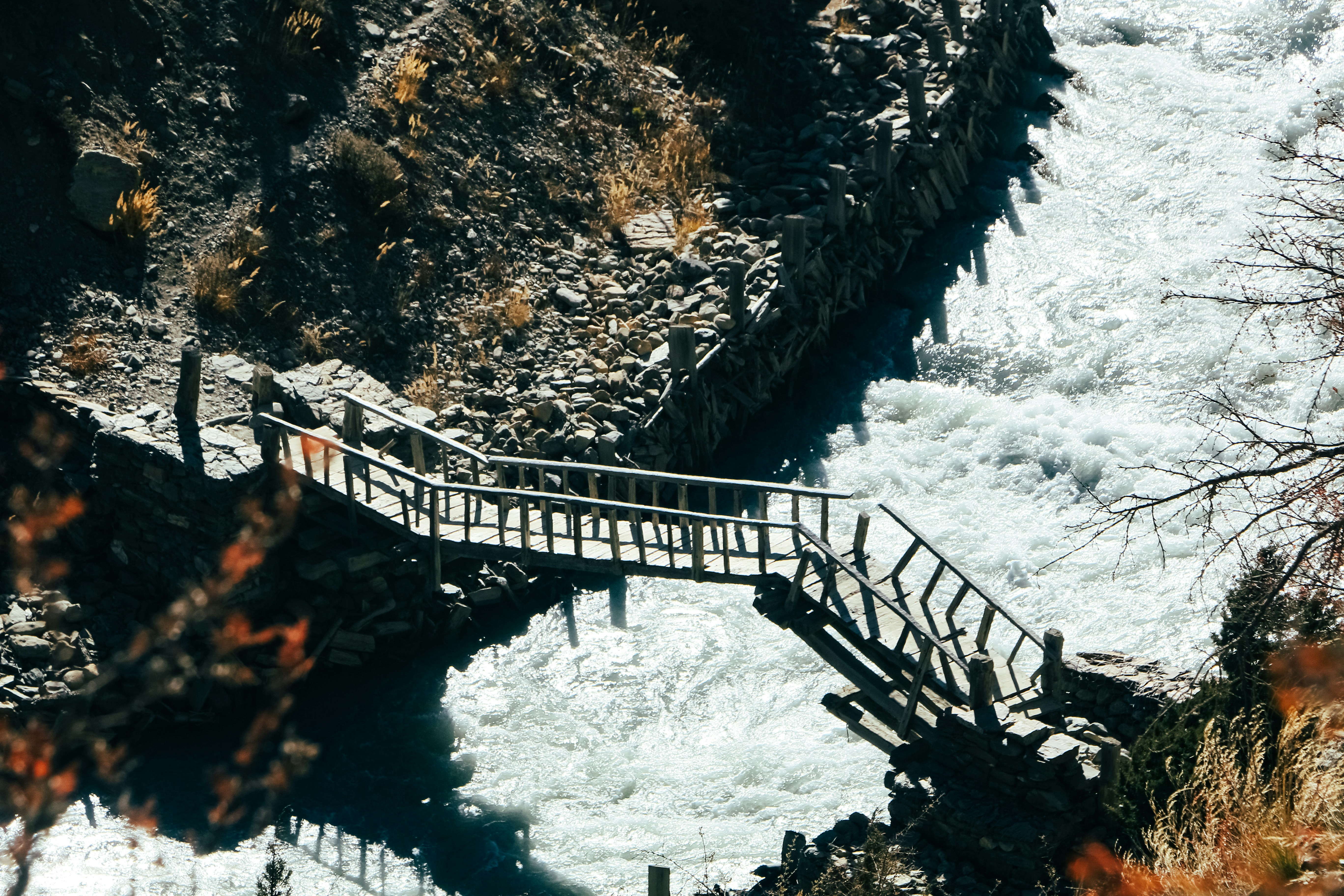 A wooden bridge over a rushing river next to a forest photo – Free ...