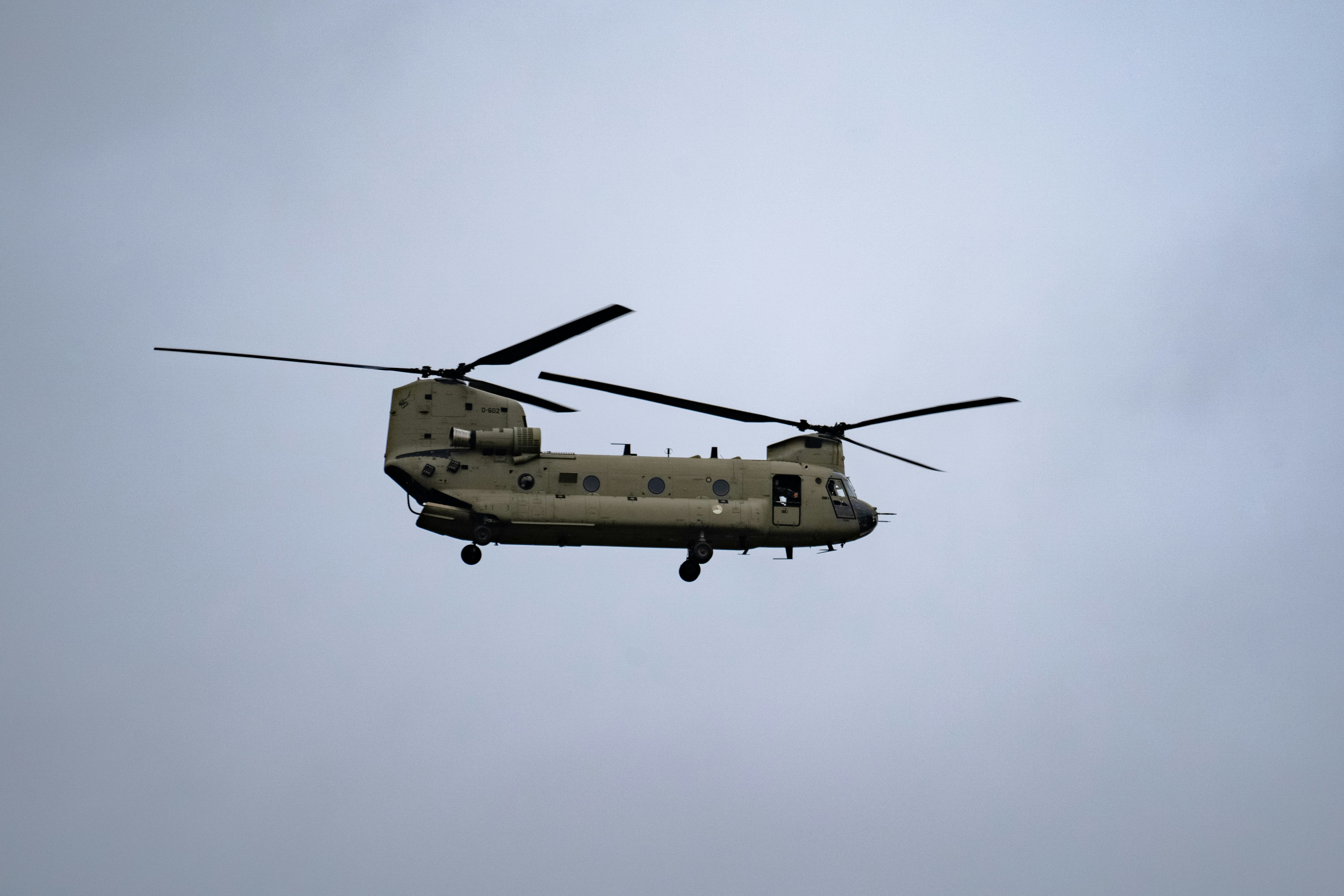 Military helicopter flying against a backdrop of grey clouds.