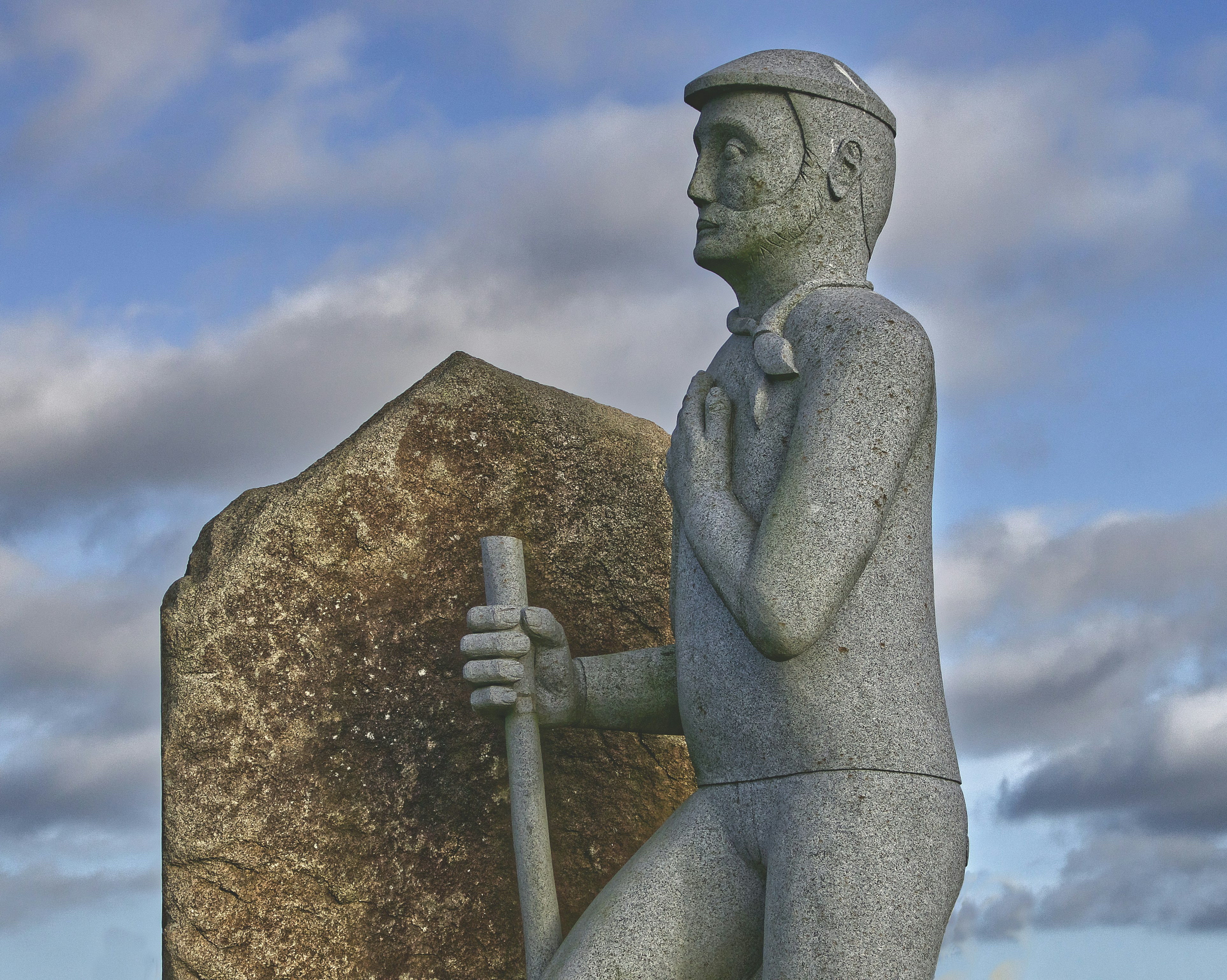 Stone Sentinel of the Cliff: A Quiet Statue Against a Clouded Sky