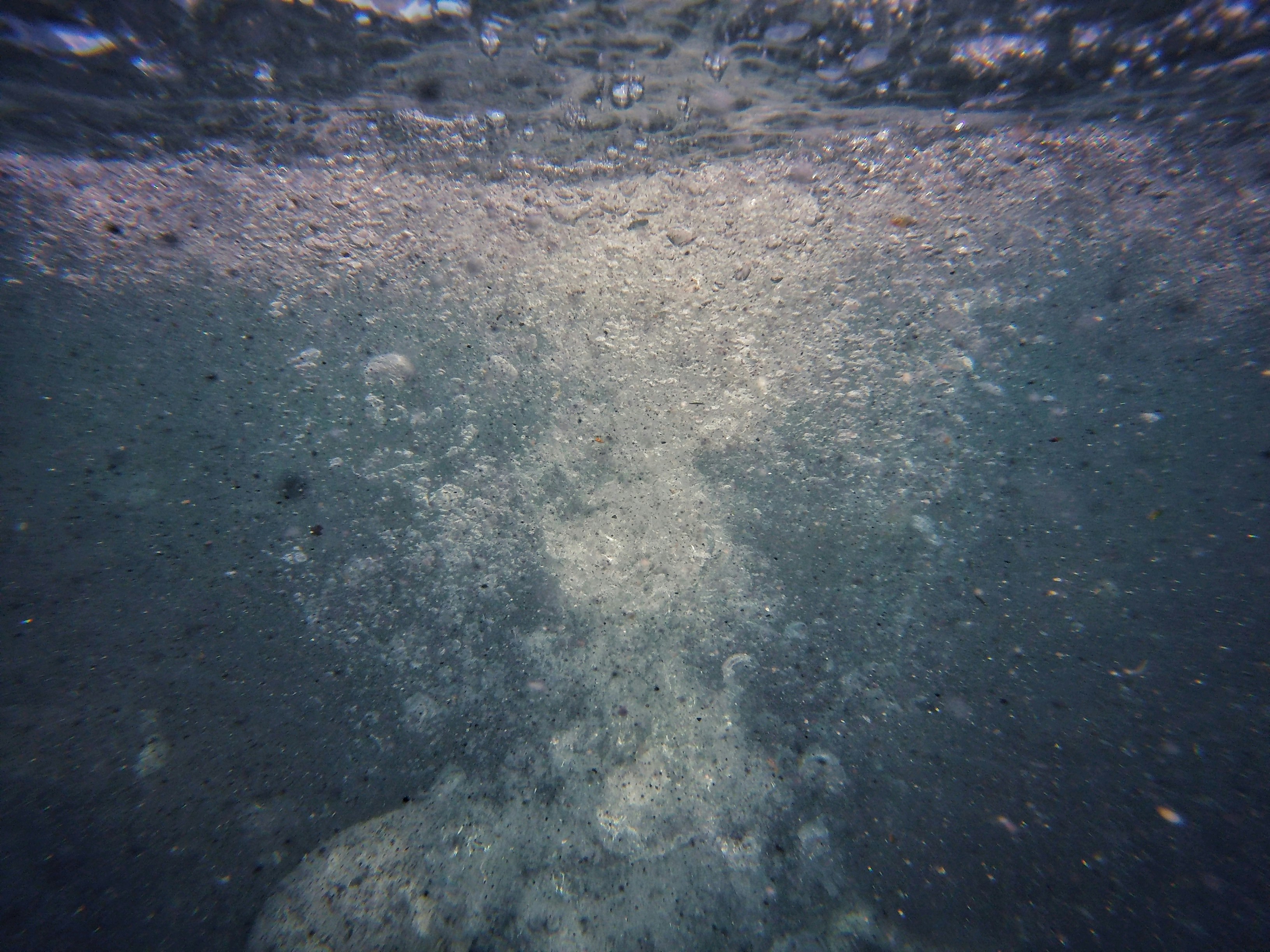 Bubbles rising through water, creating a mesmerizing effect against a sandy bottom. The image captures the dynamic interaction between air and water.