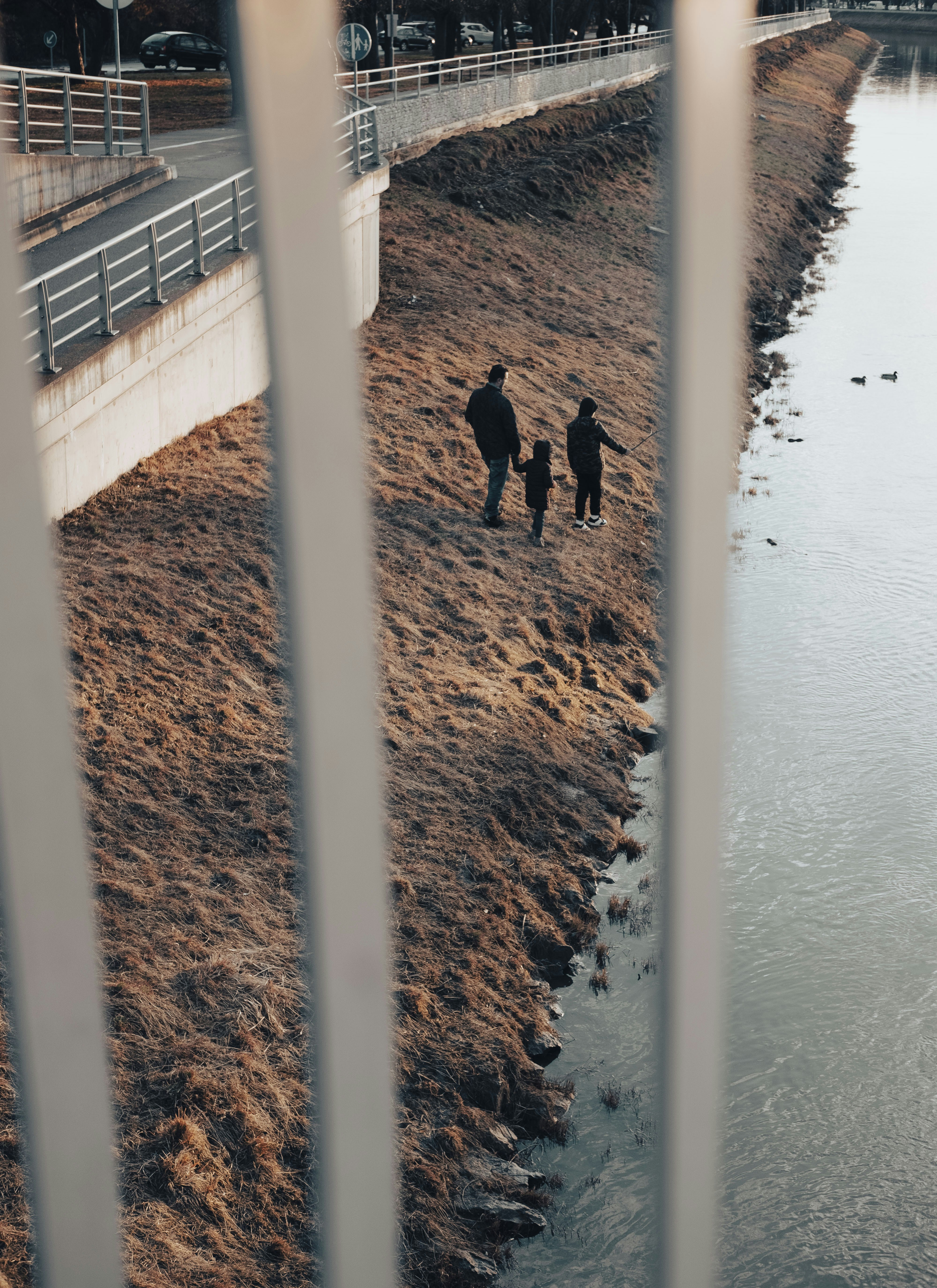 Three figures by the riverbank, framed by vertical rails
