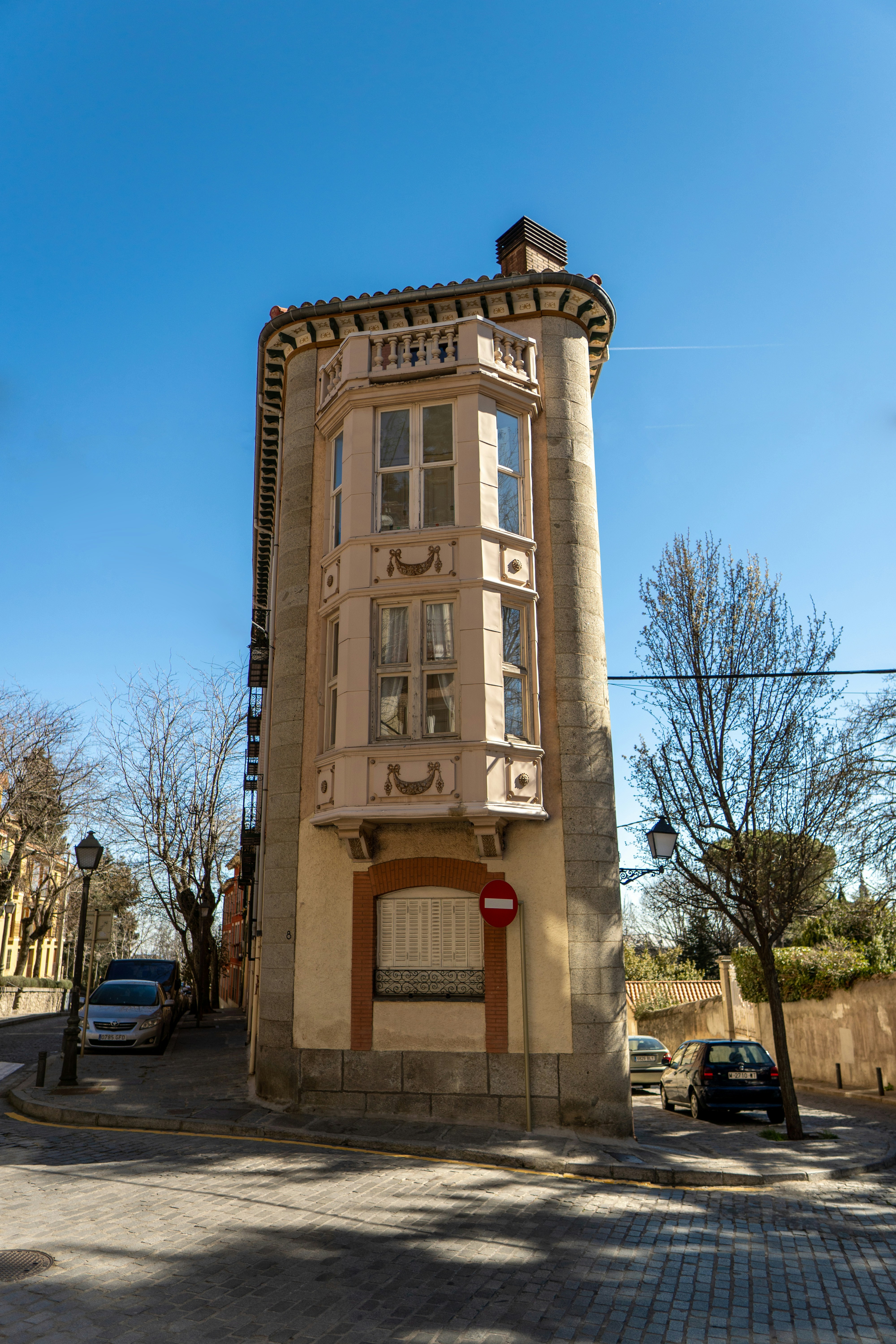 Unique building with a rounded facade and large windows, nestled at the corner of a cobblestone street. A clear blue sky serves as a backdrop.