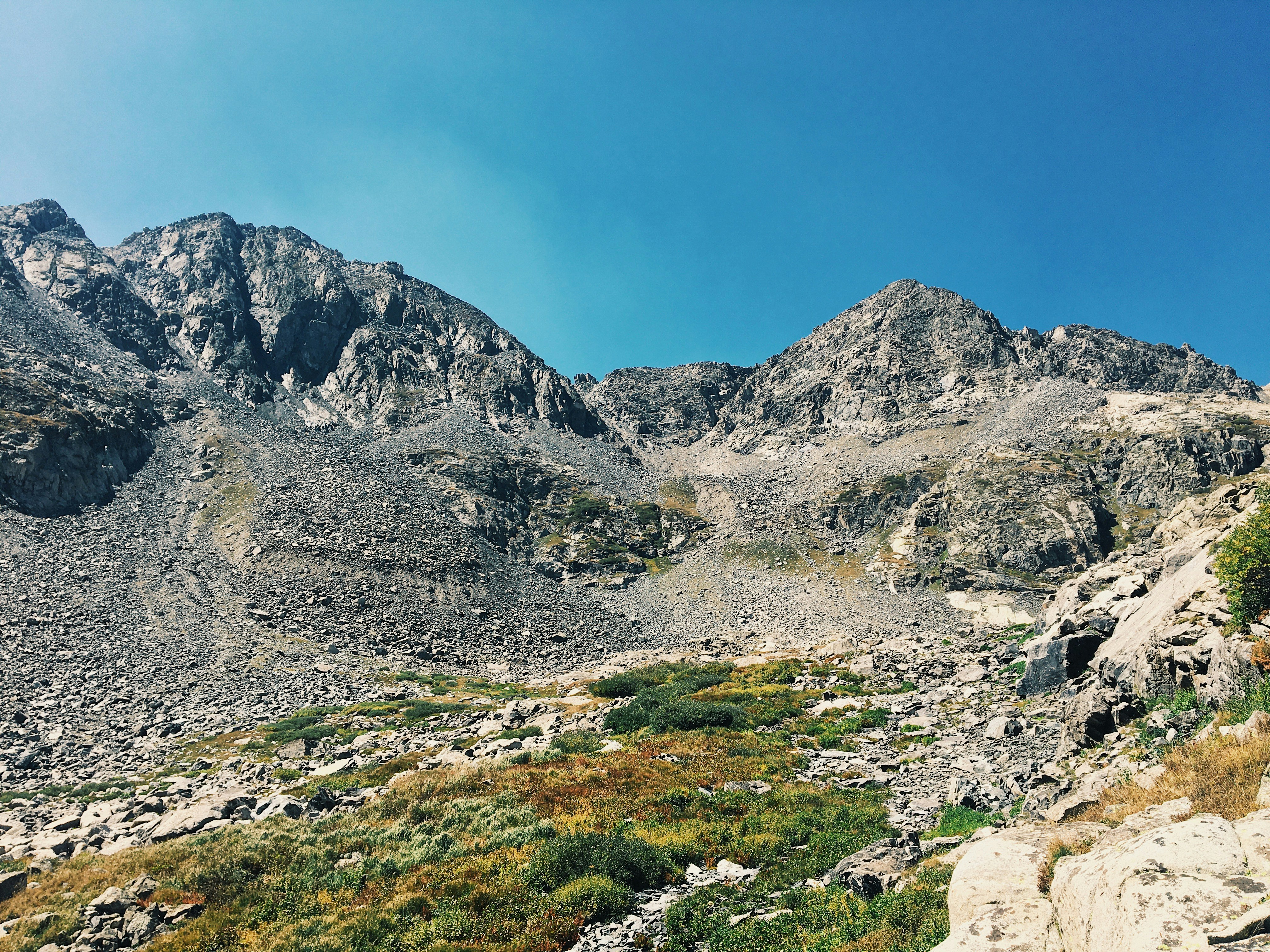 Rocky mountain landscape with a clear blue sky, showcasing rugged terrain and sparse vegetation.