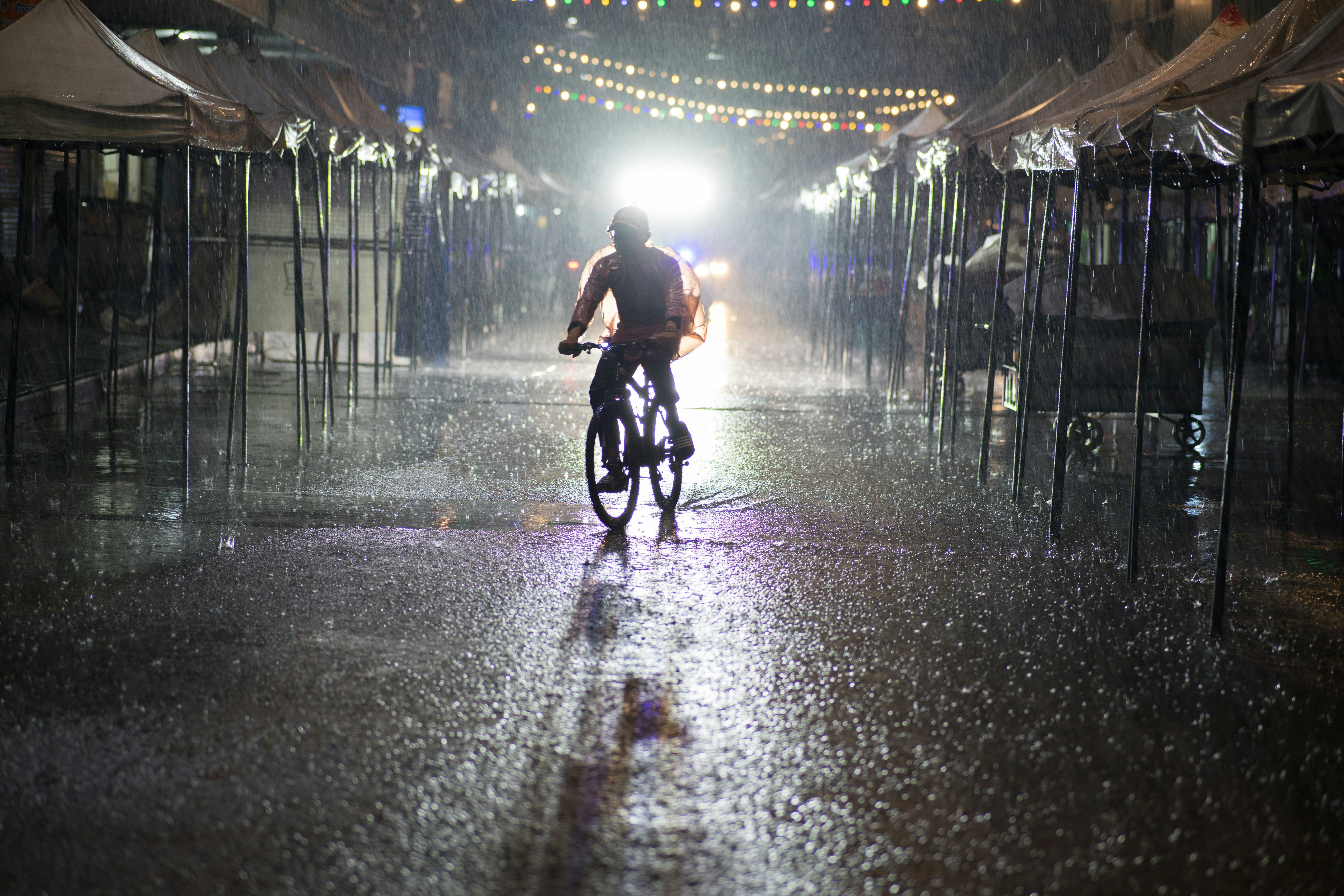 A man riding a bike down a rain soaked street photo – Free Bangkok ...