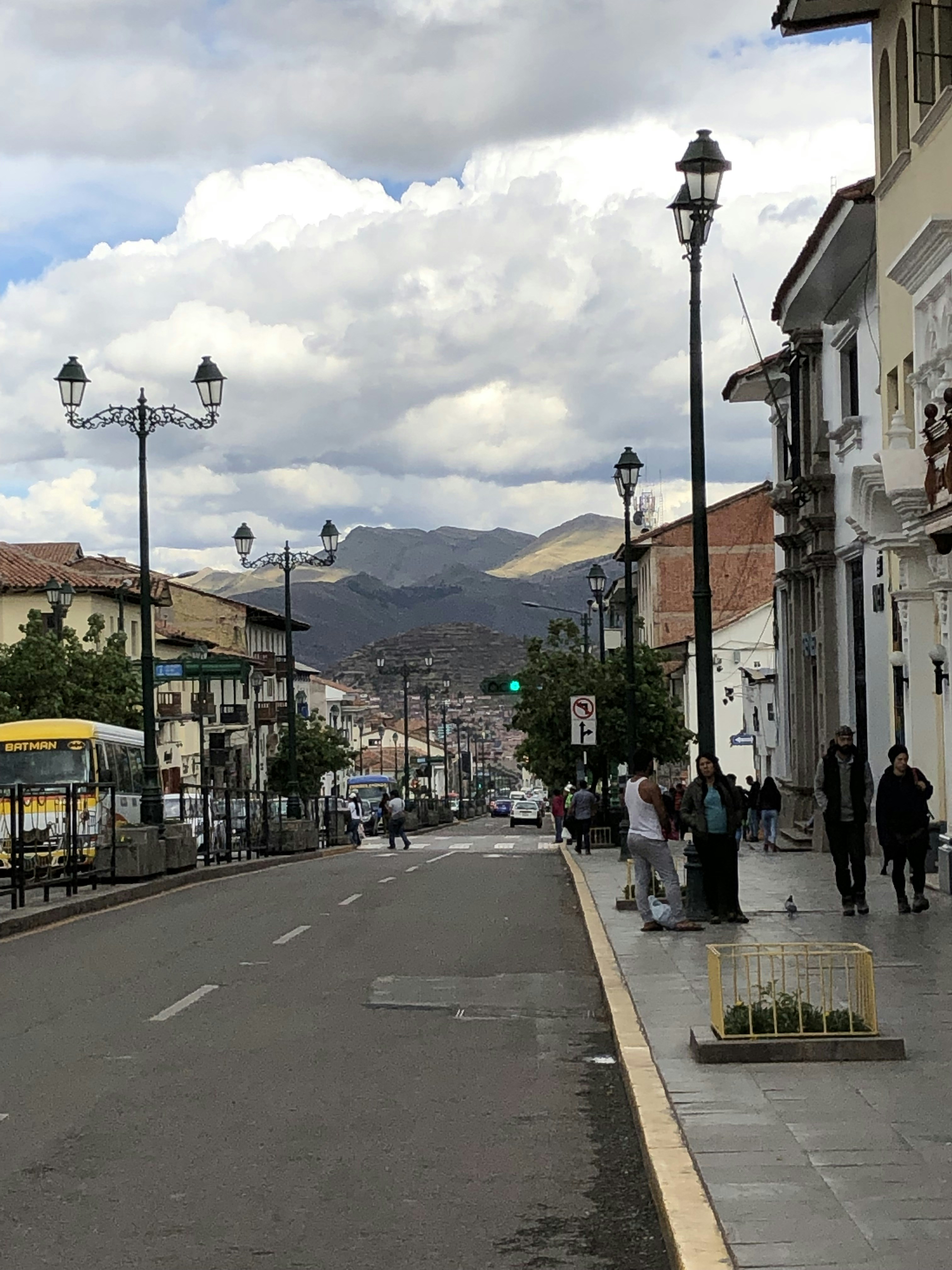 Bustling street scene in Cusco, showcasing colonial architecture and vibrant local life, with mountains framing the backdrop. 