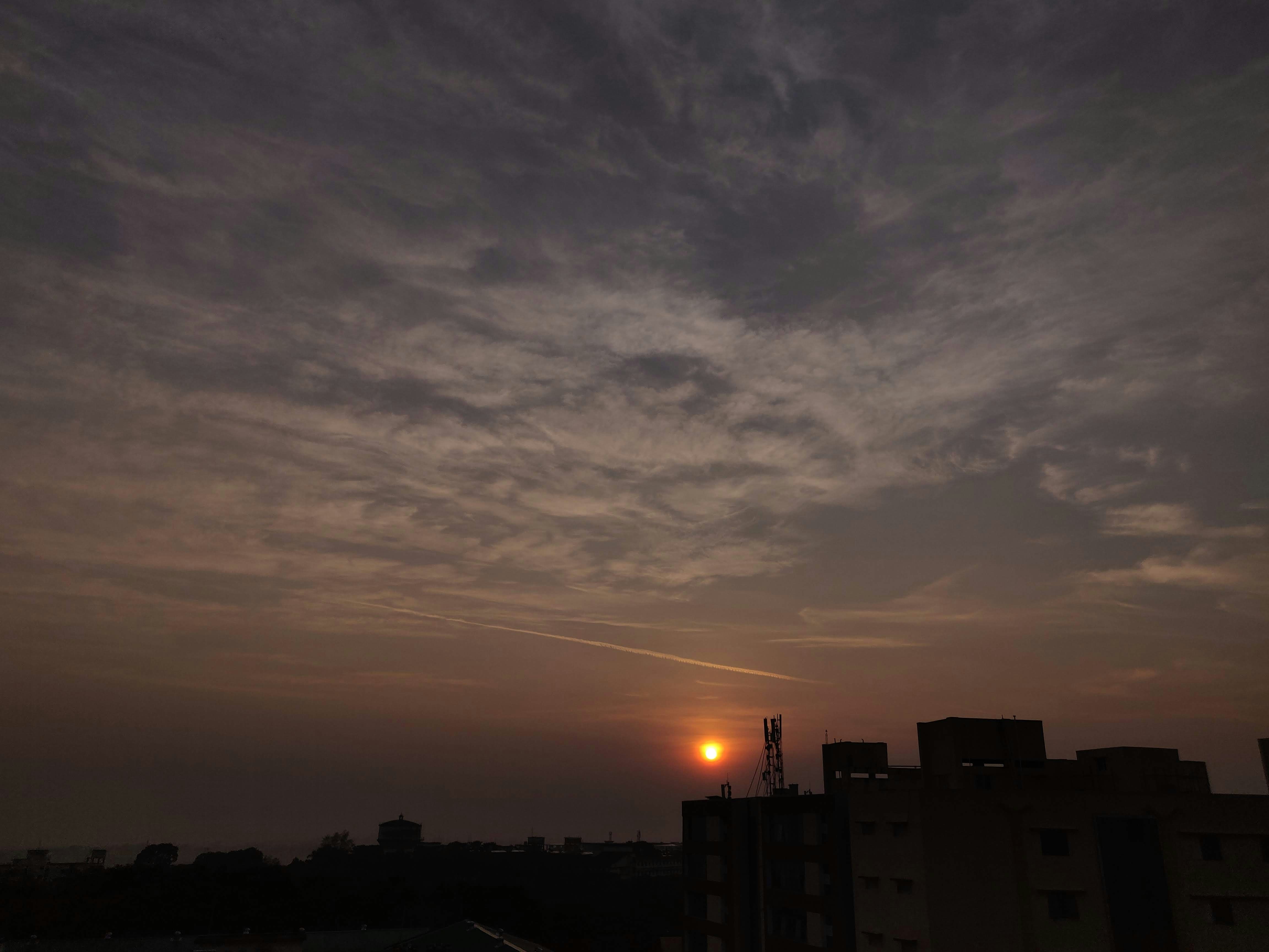 Sunset casting a warm glow behind silhouetted buildings, with wispy clouds creating a tranquil atmosphere.