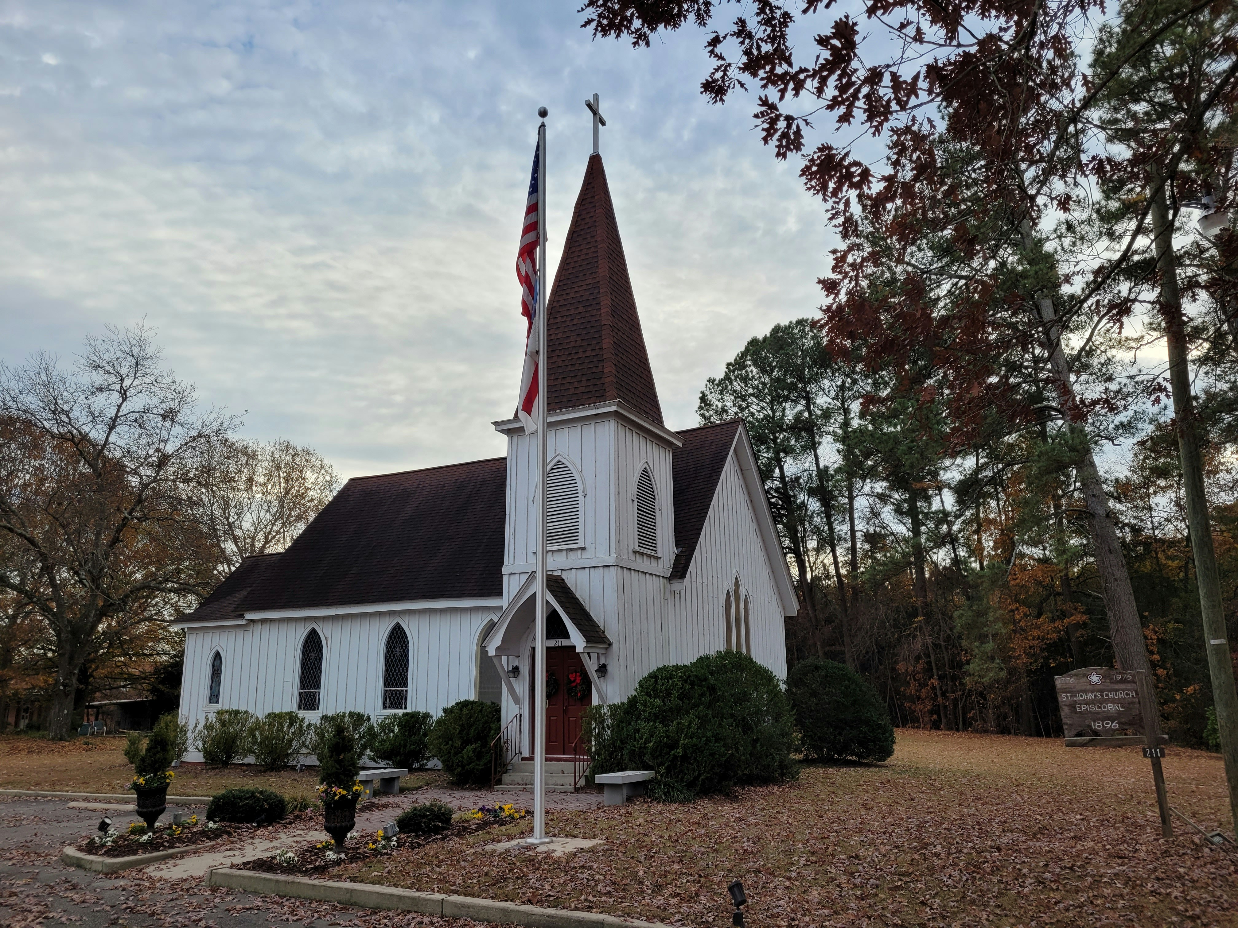 White wooden church with a steep roof and a tall steeple, framed by autumn foliage and flagpoles. The scene evokes a sense of tranquility and community.