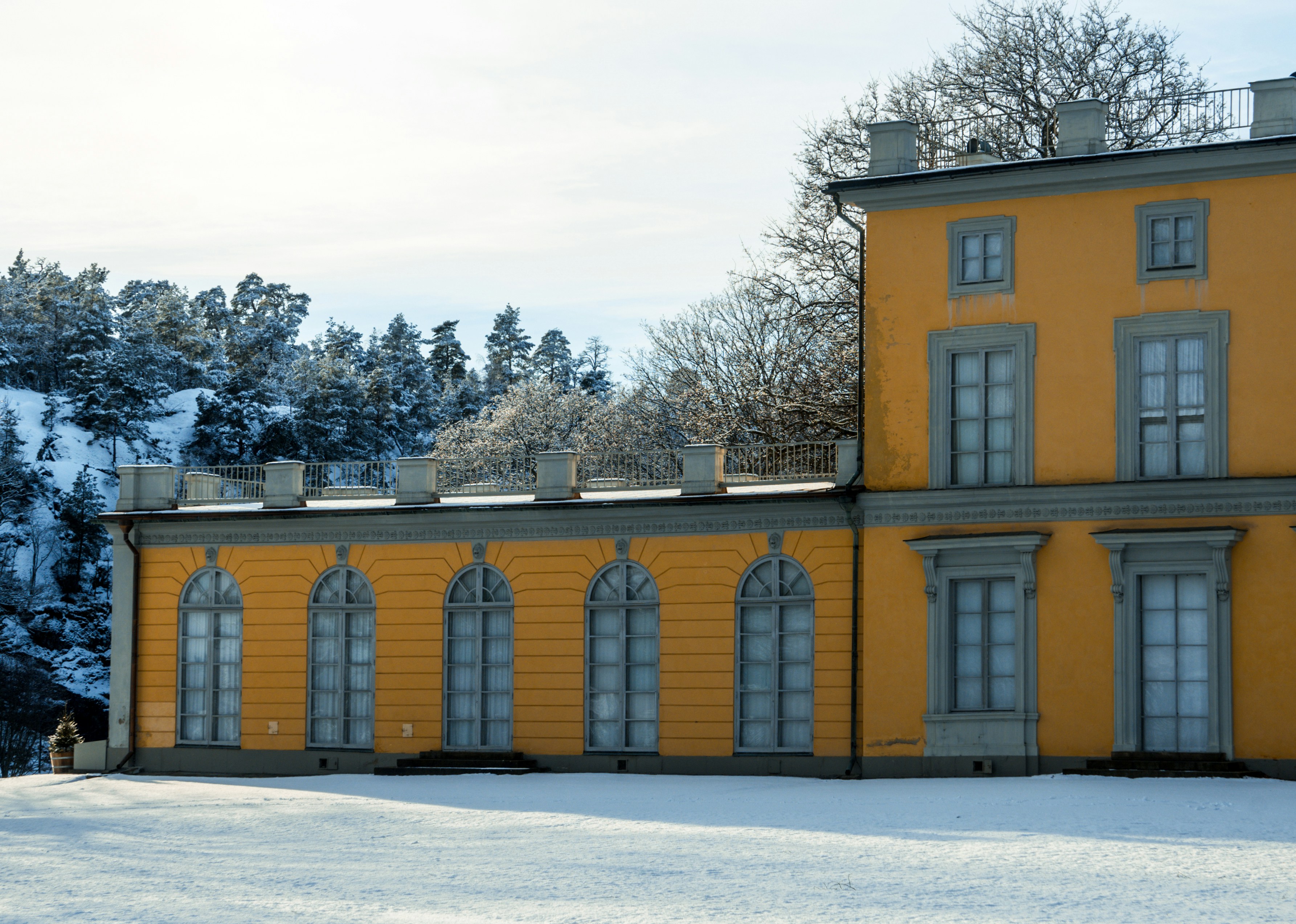 Large yellow building framed by snow-covered ground and frosty trees.