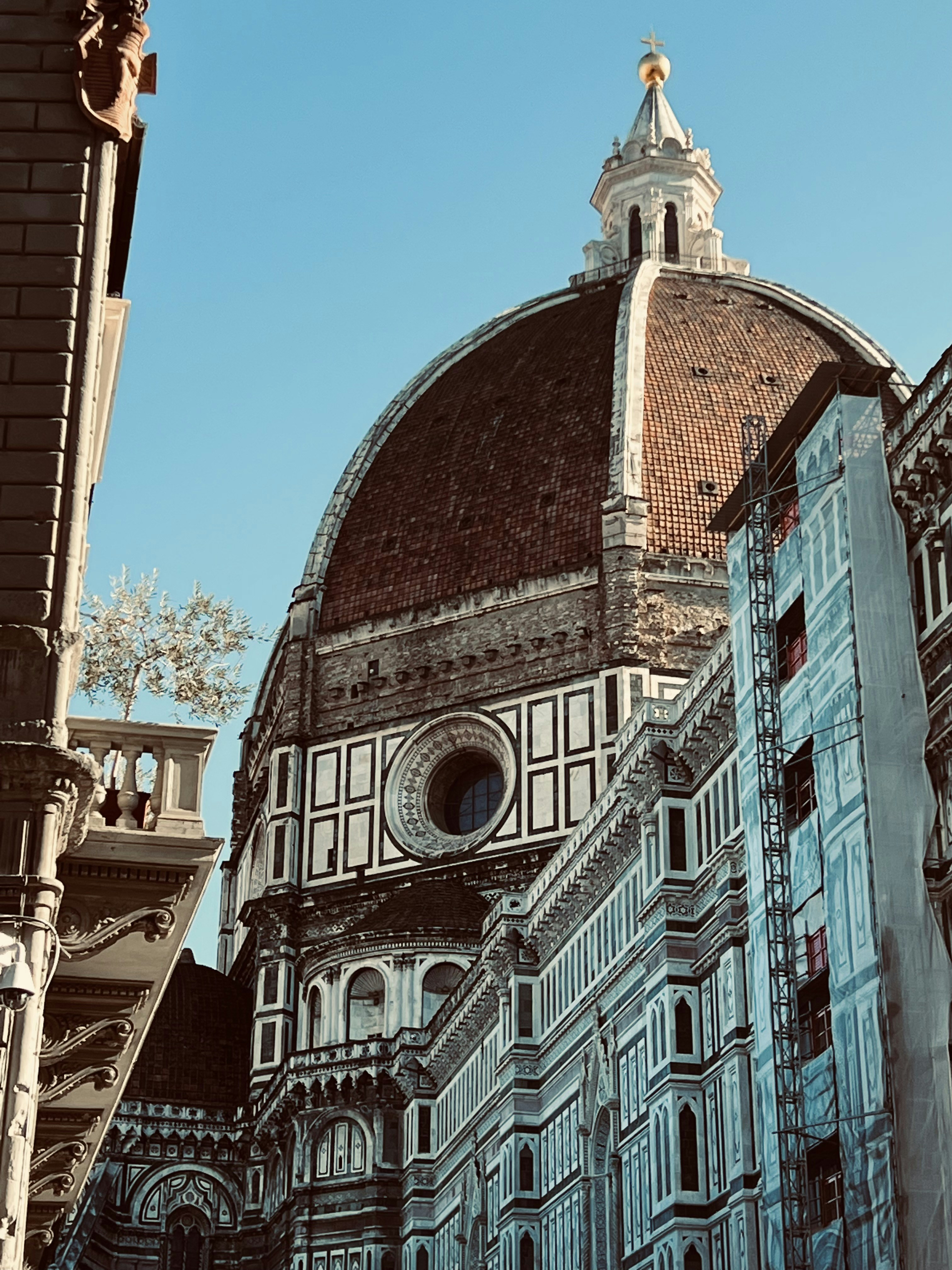 Historic dome with intricate stonework and a cross atop, framed by adjacent ornate buildings under a clear blue sky.