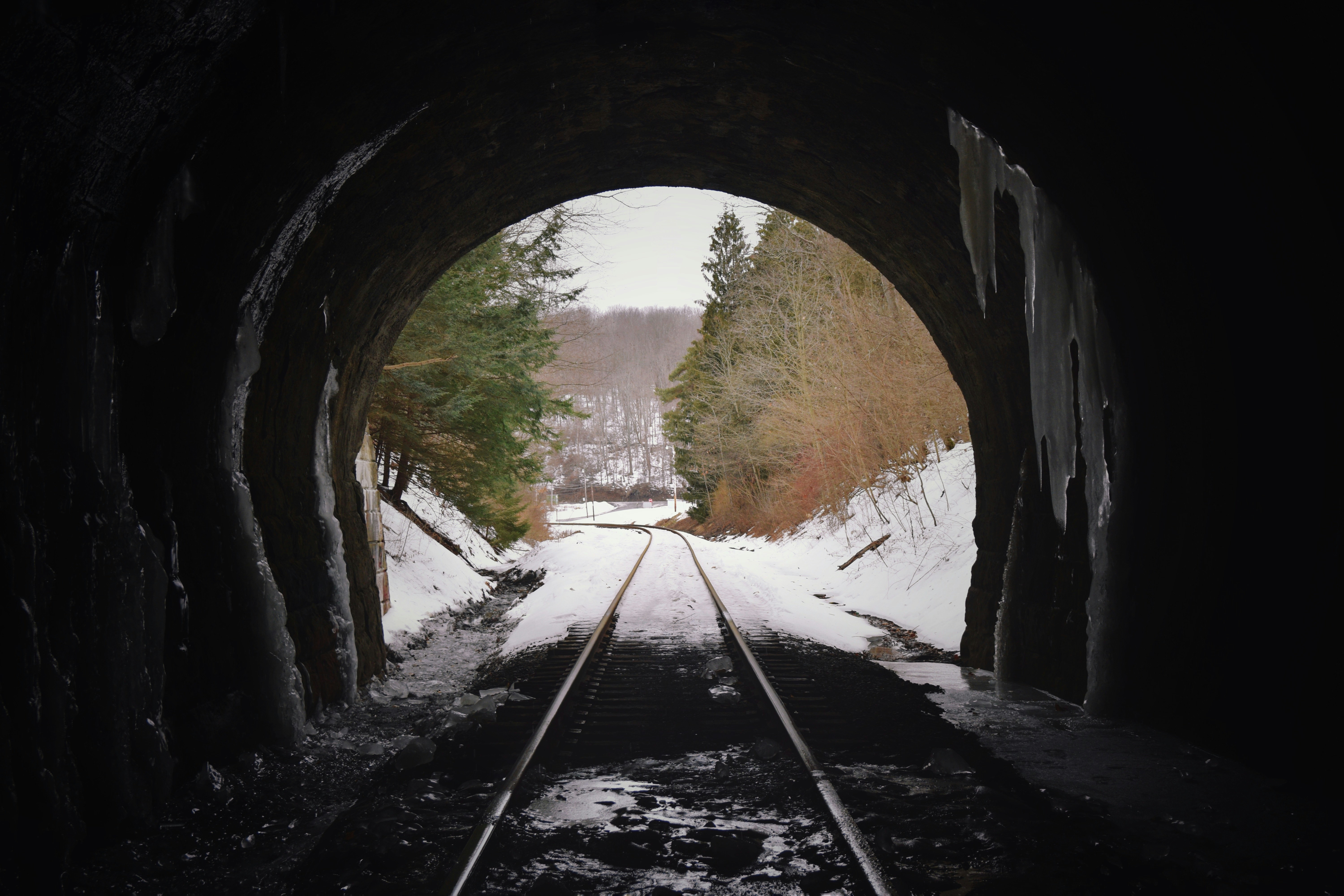 View from inside a snow-covered tunnel, revealing a glimpse of the railway and the winter landscape beyond. Icicles hang from the tunnel's edges.
