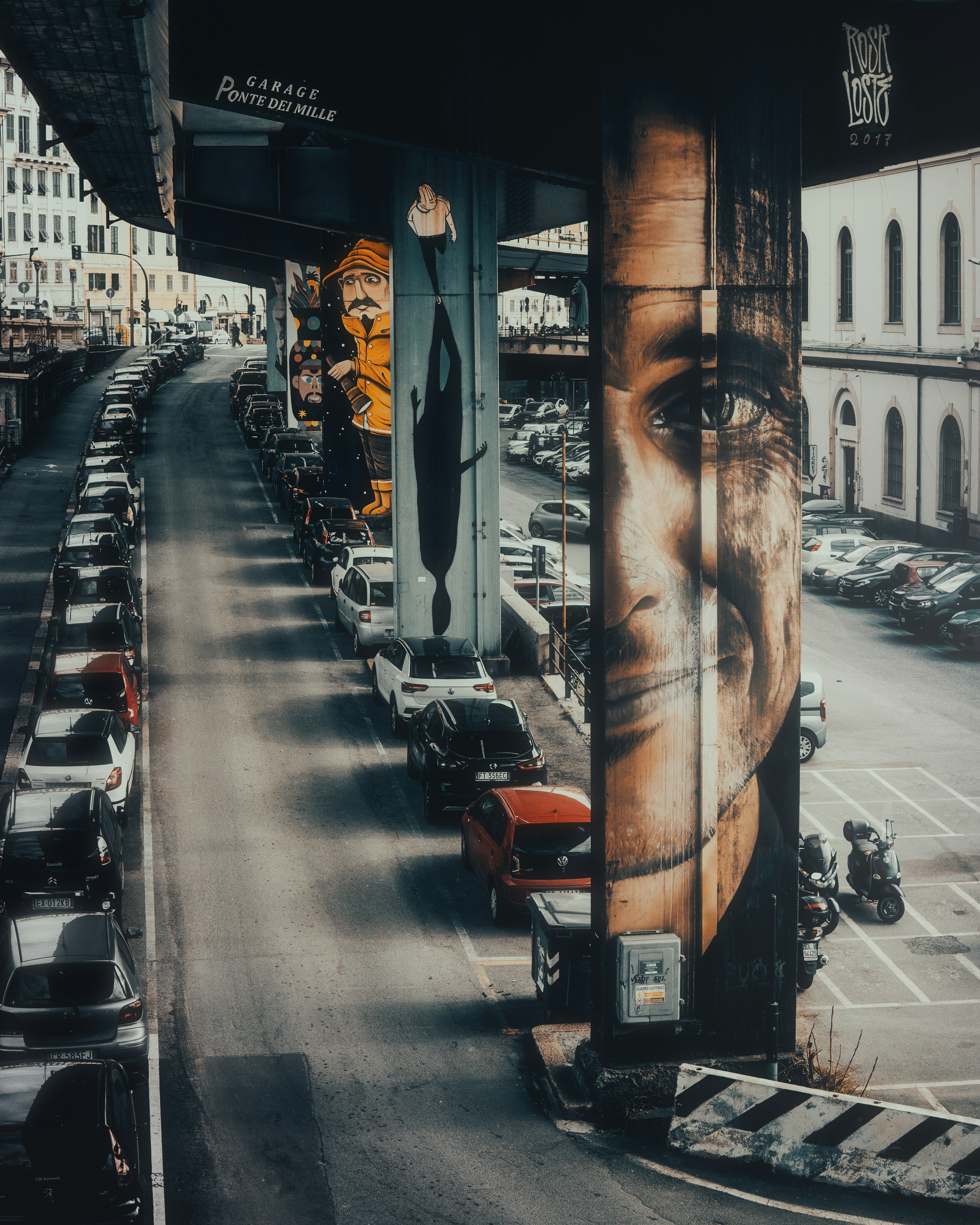 Concrete Portraits Under the Overpass: A Car-Lined Street Framed by Mural Giants