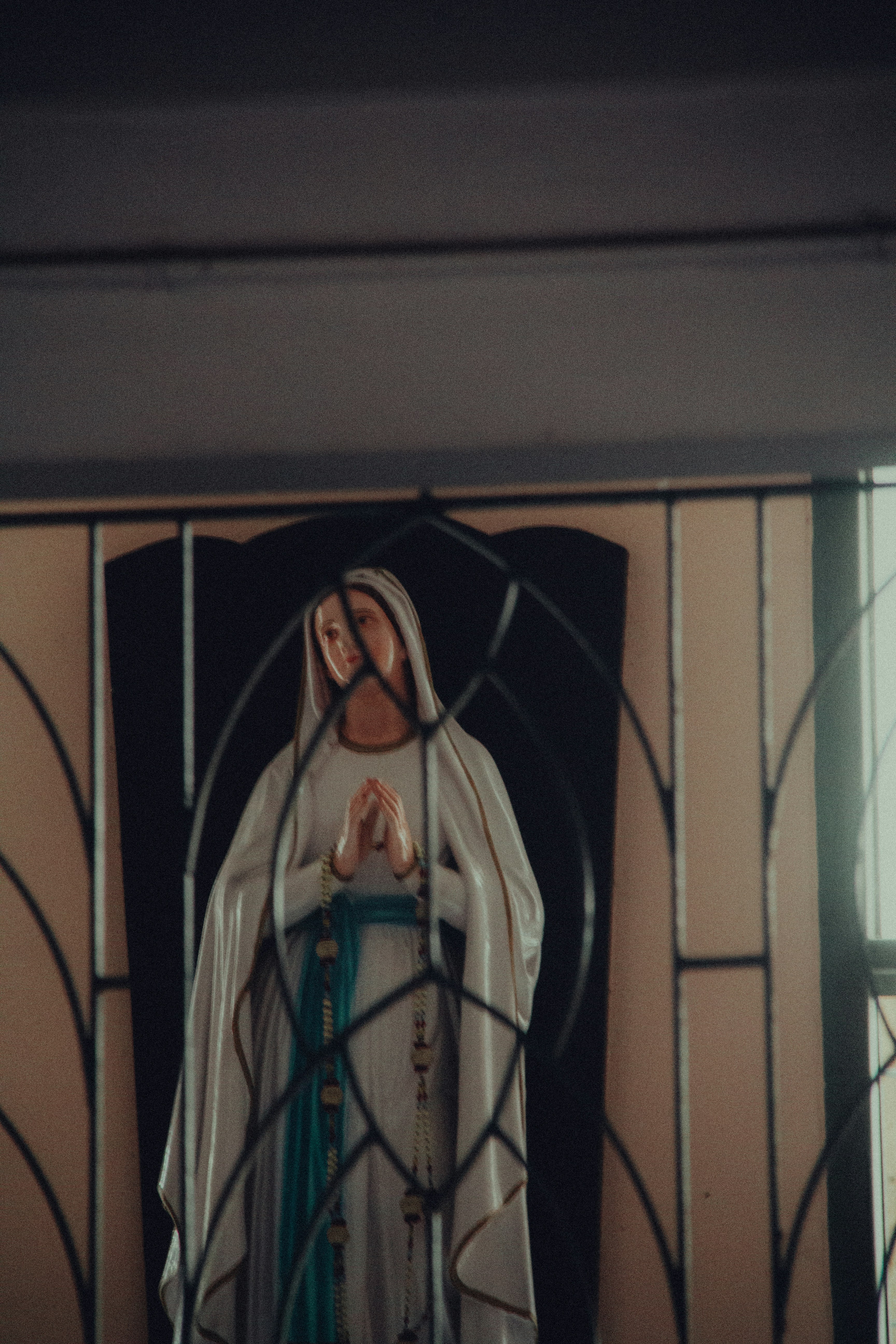 Statue of a serene figure in prayer, framed by intricate ironwork, capturing a moment of reflection and devotion.