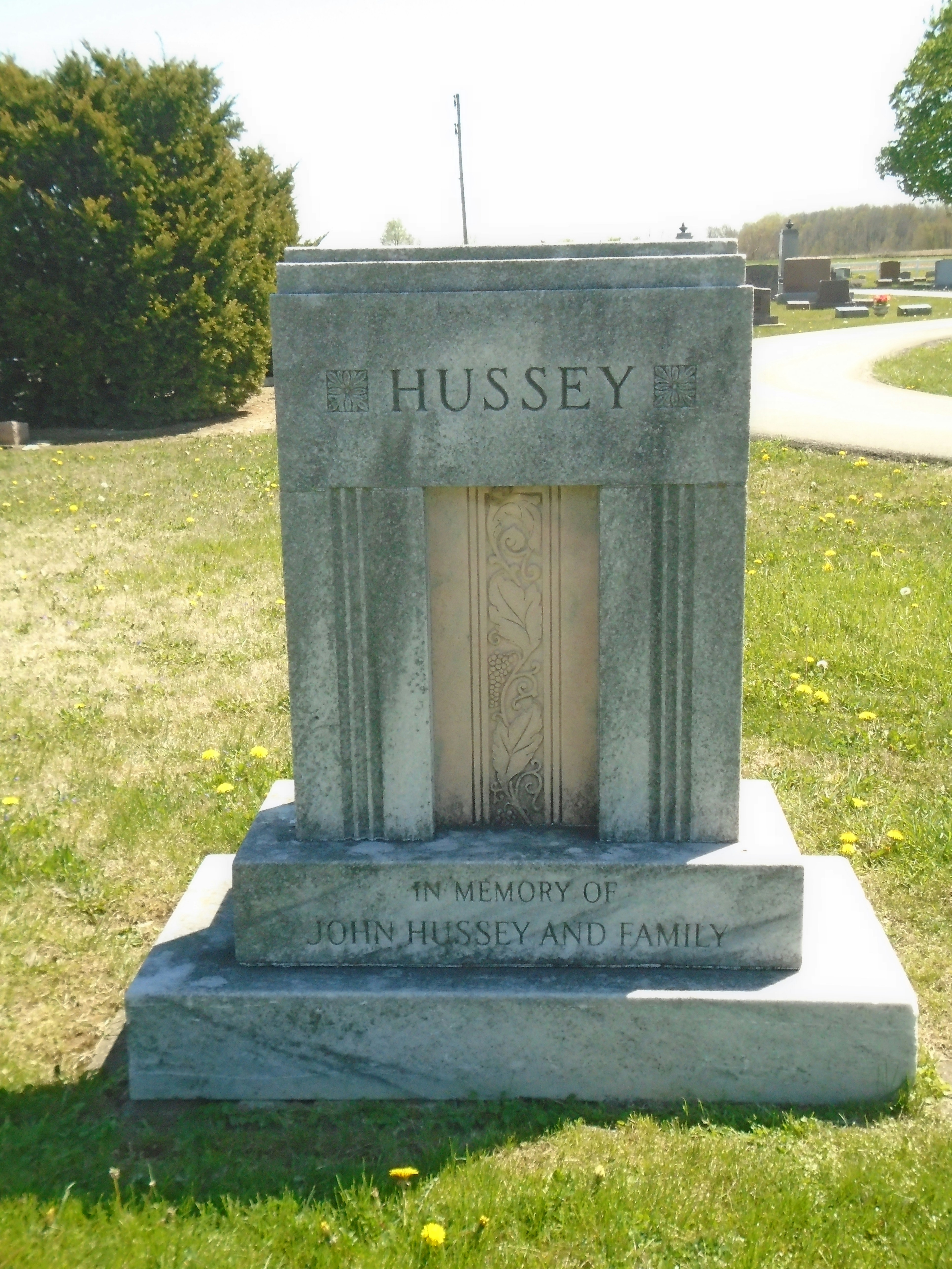 Elegant gravestone honoring John Hussey and family, surrounded by lush grass and trees in a serene cemetery setting.