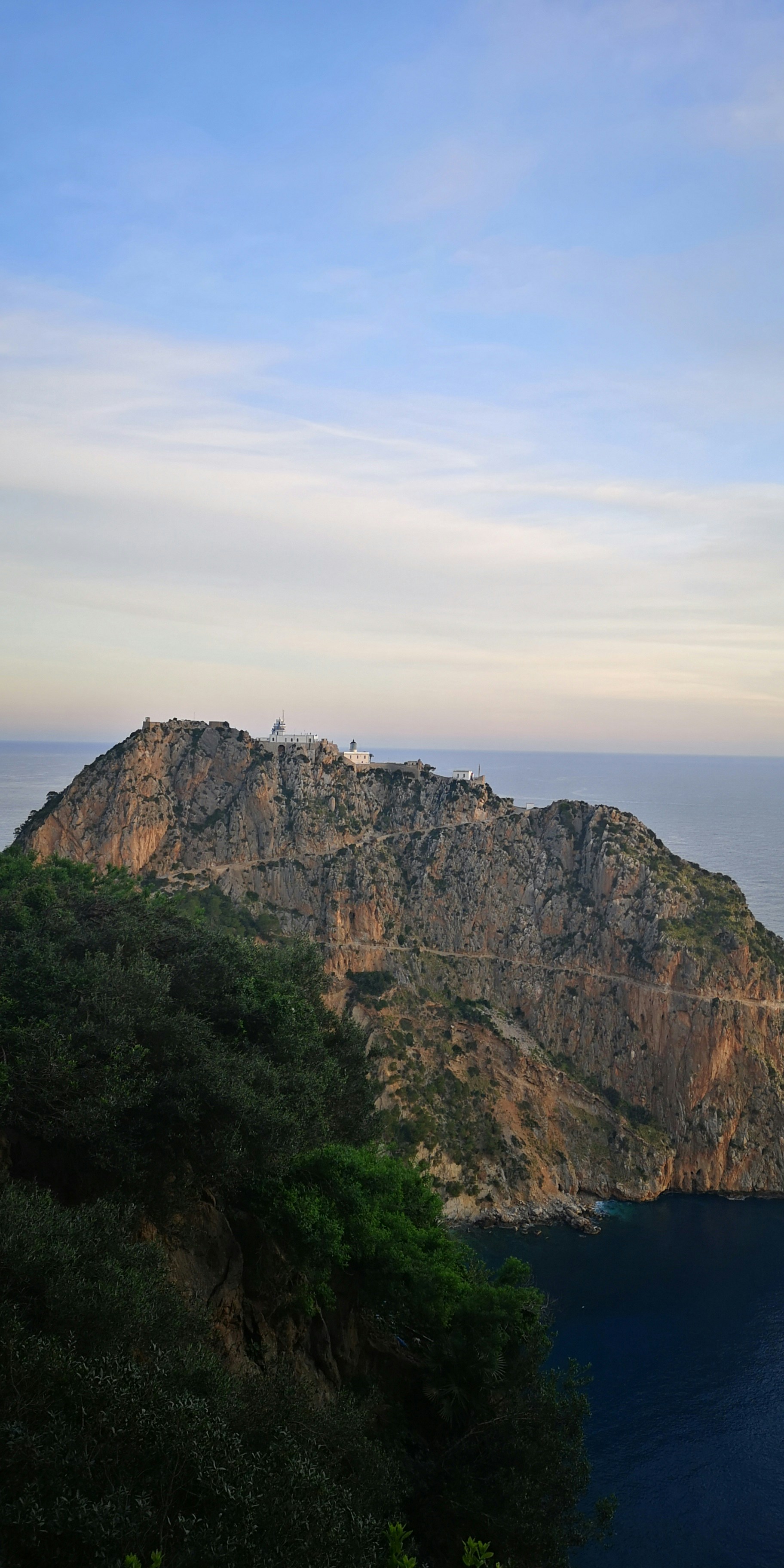 A rugged coastal cliff with a distant settlement perched atop, overlooking the serene sea. The scene captures the harmony between nature and human habitation.