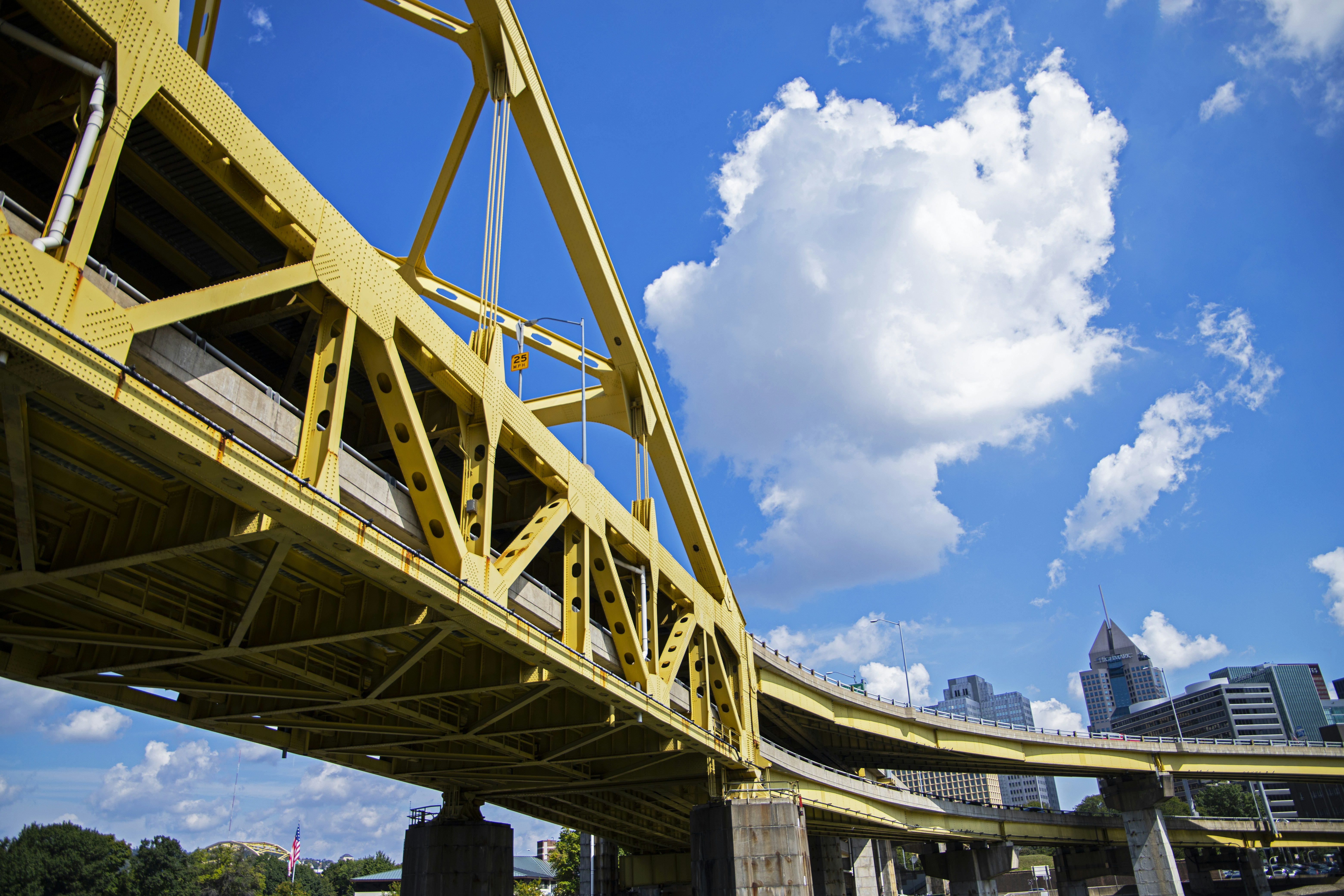 A large yellow bridge over a river with tall buildings in the ...