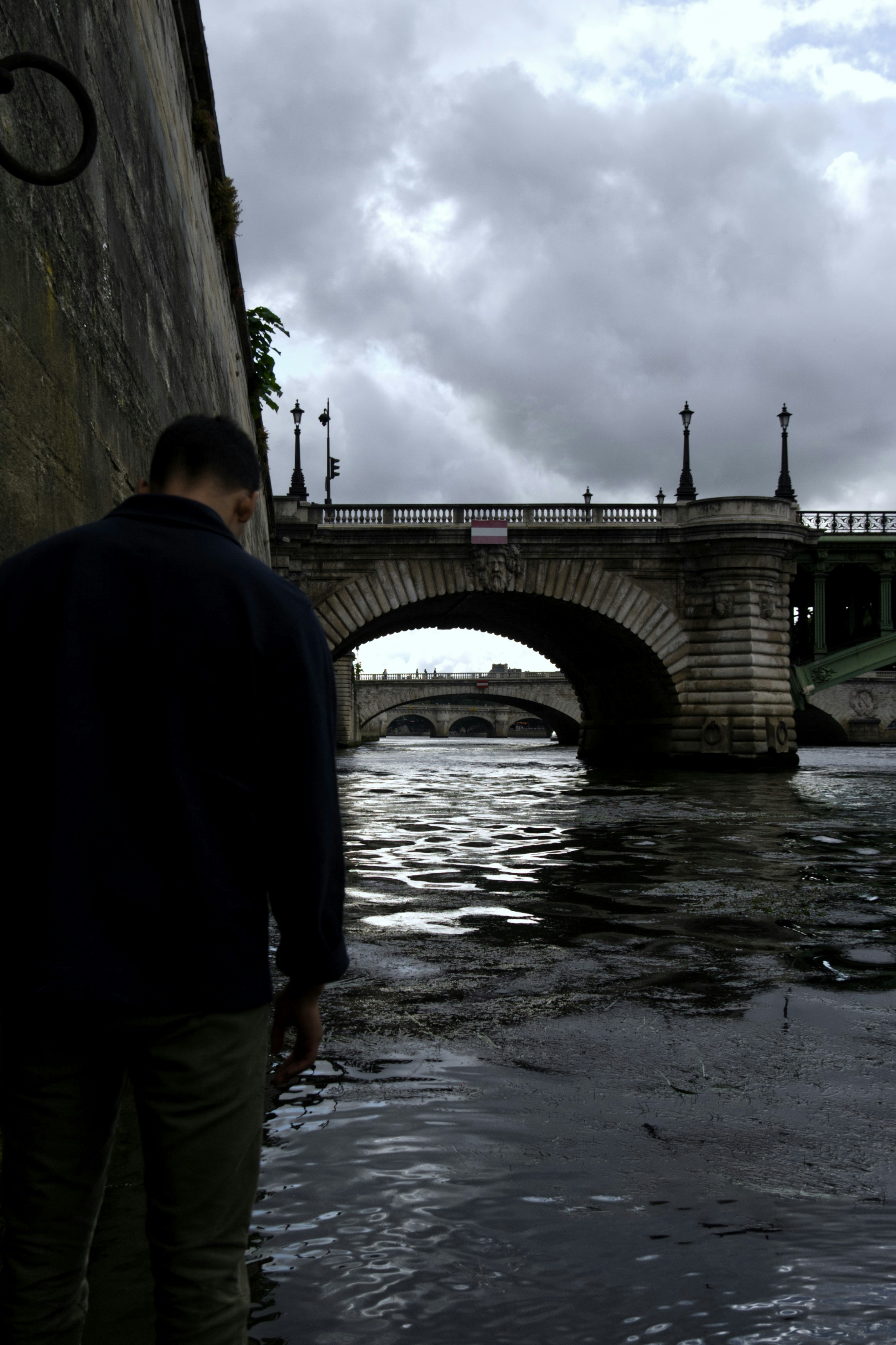 Shadow on the Riverbank: Silhouette Beneath the Arched Bridge