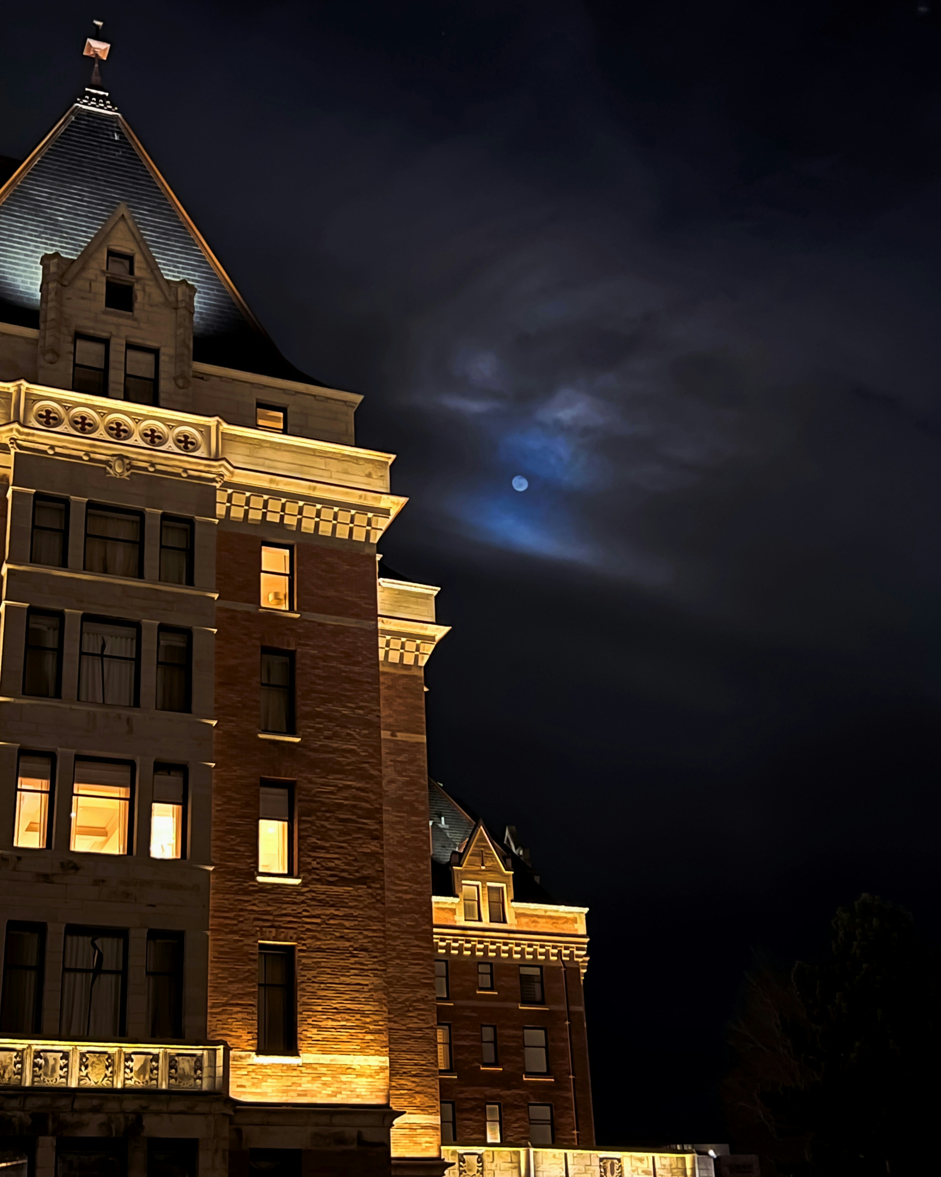 Historic building illuminated against a dark sky, showcasing intricate architectural details and a hint of moonlight peeking through clouds.