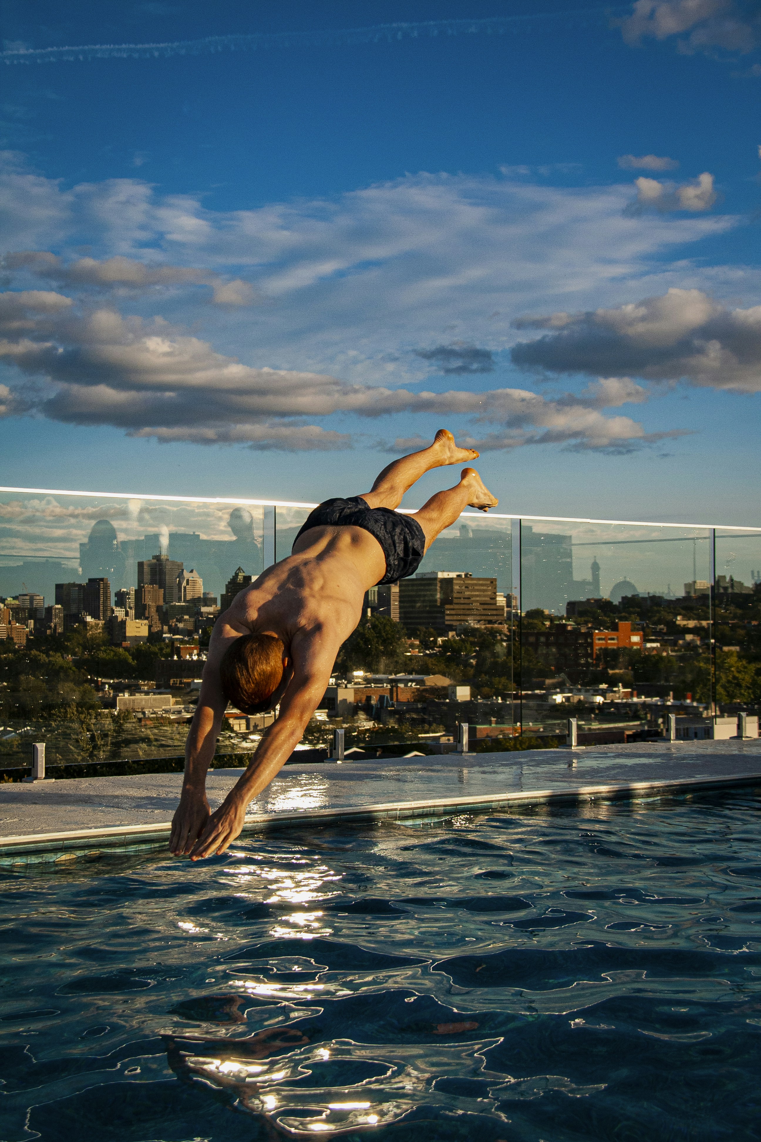A man diving into a swimming pool with a city in the background photo ...