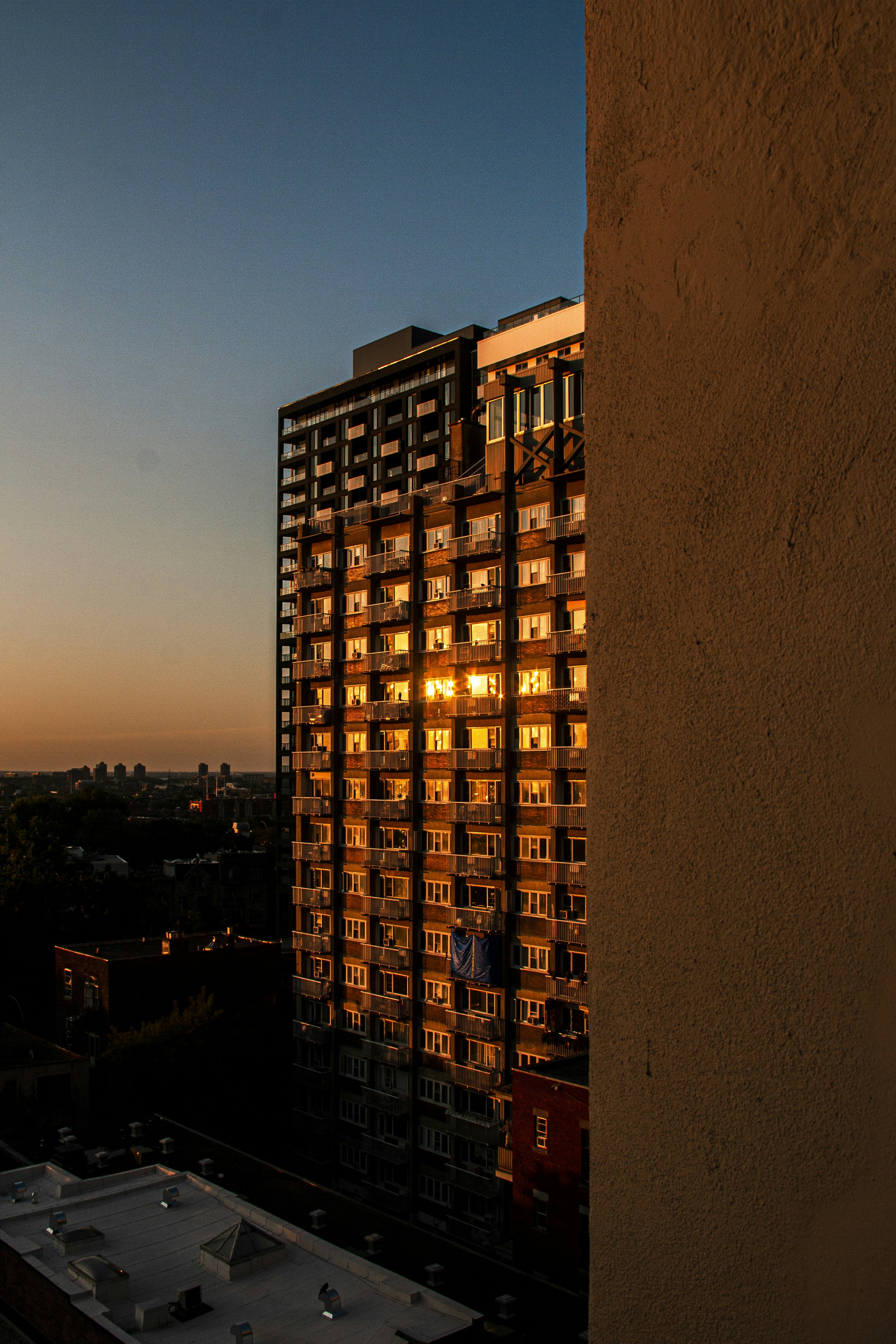 Sunlight reflecting off the windows of a high-rise building during sunset, framed by a concrete wall. The warm tones create a striking contrast against the cool evening sky.