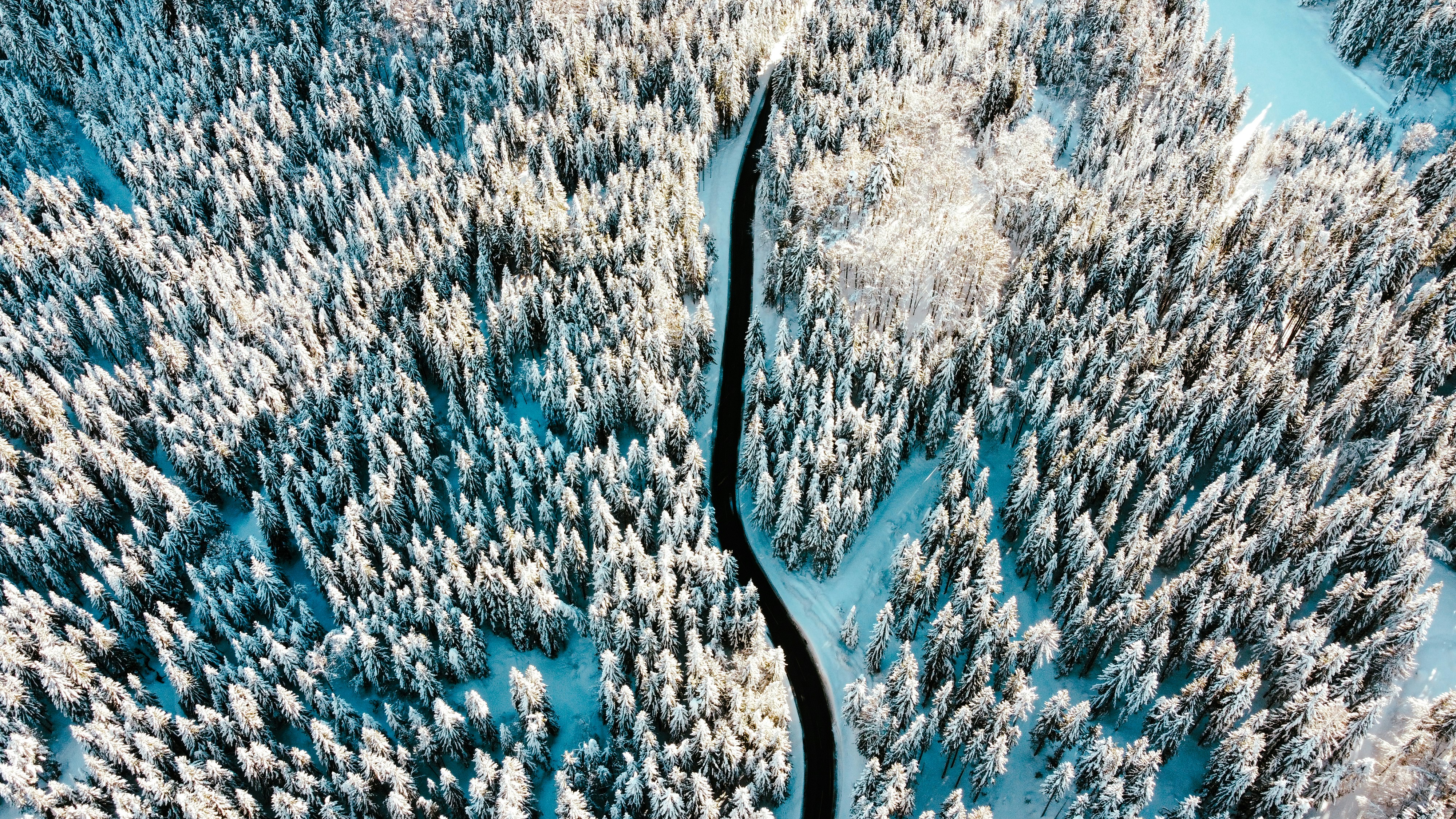 A serene river meanders through a snow-covered forest, showcasing the tranquil beauty of winter's landscape.