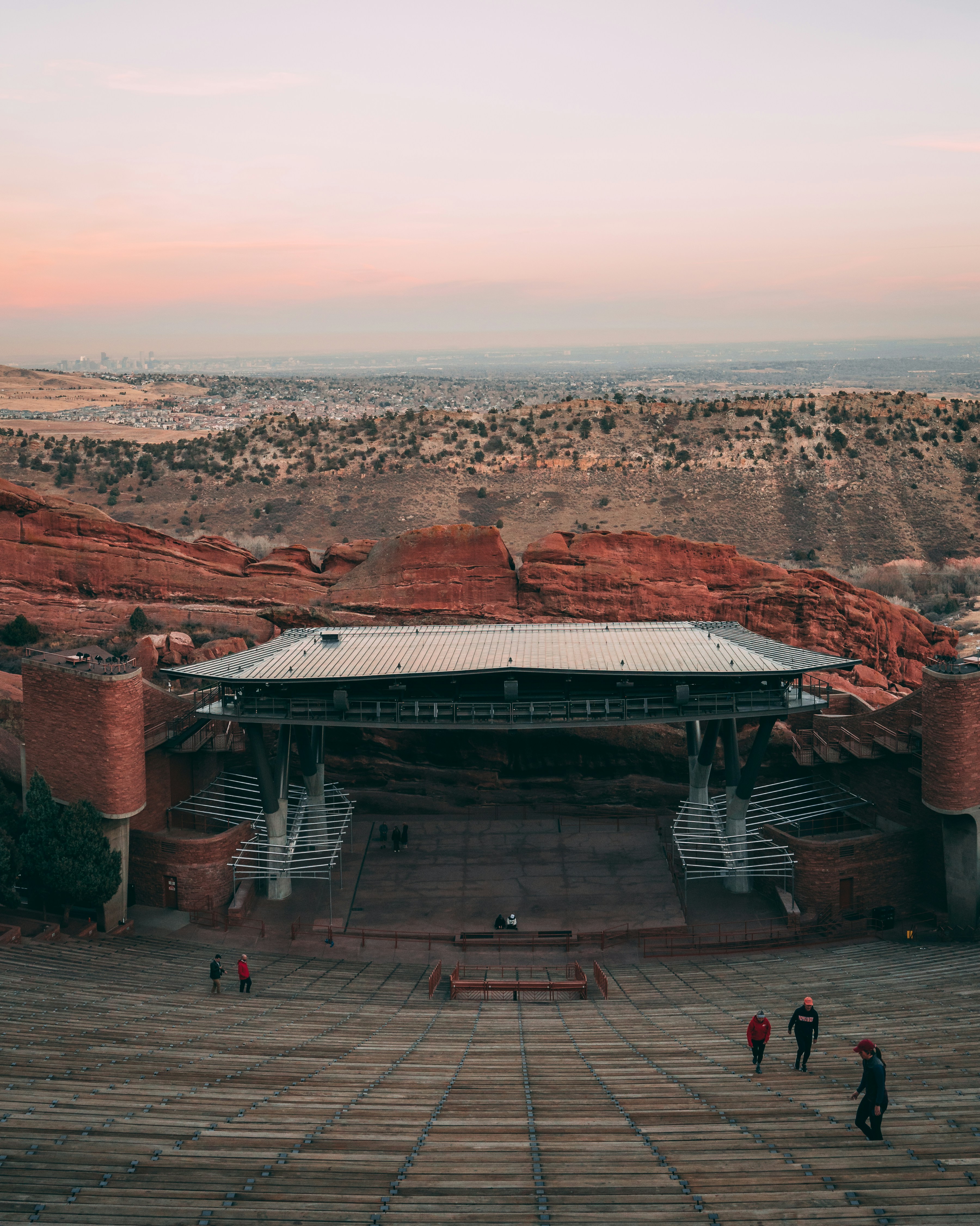 Open-air amphitheater nestled among red rock formations with a panoramic view of the landscape. Visitors explore the venue as dusk settles in.