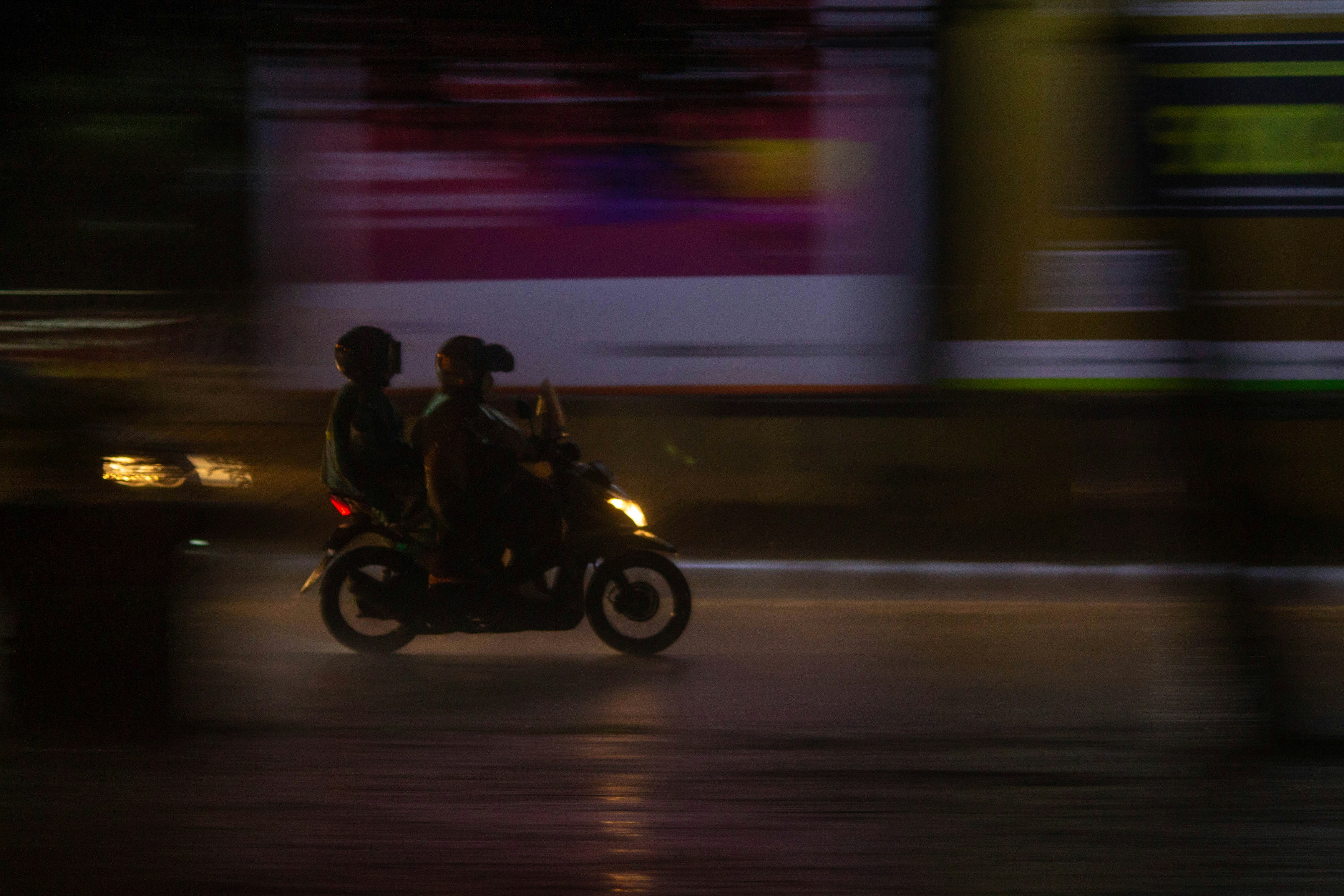 Motorbike with two riders moving swiftly through a dimly lit street at night.