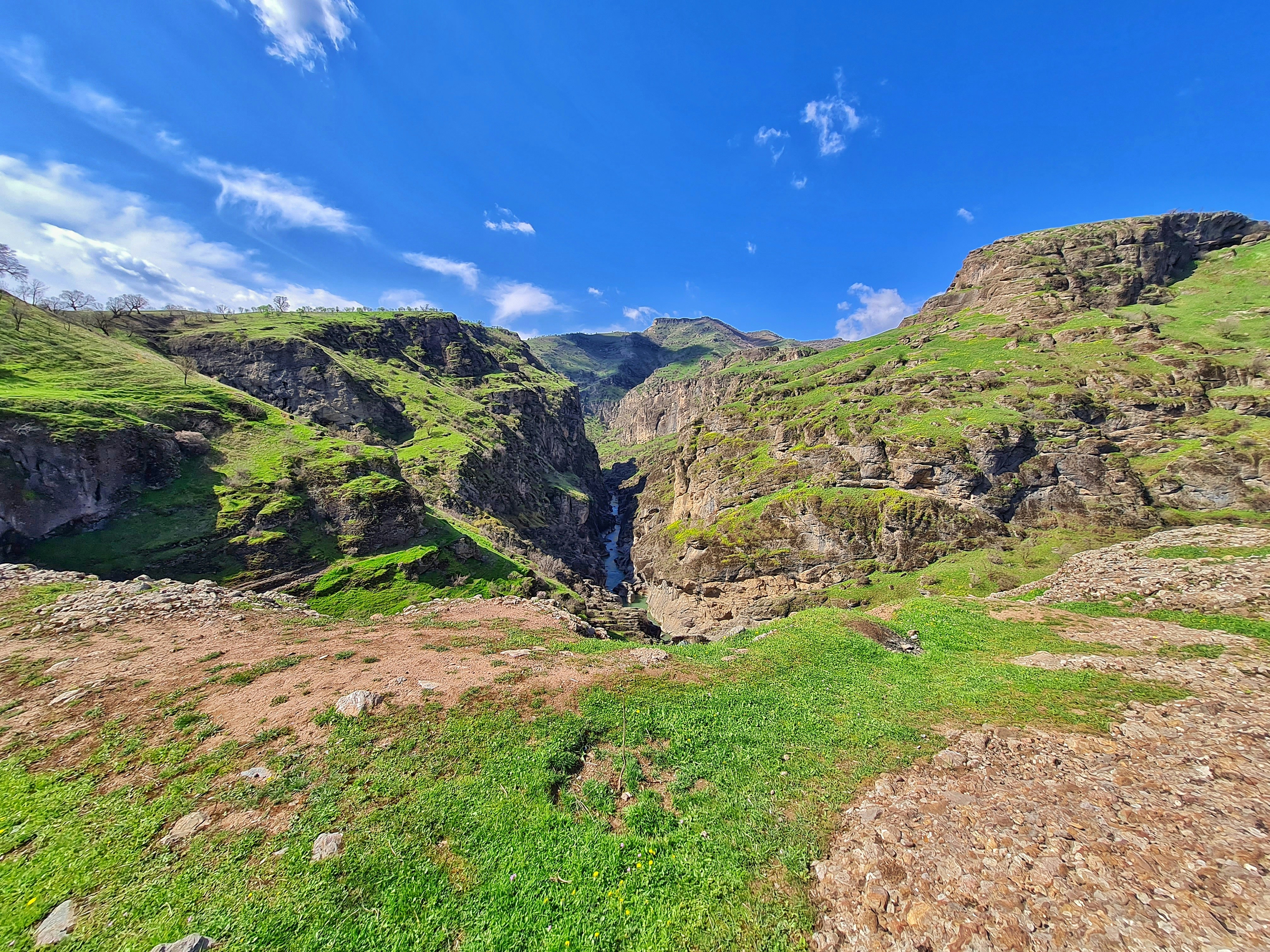 Lush green valleys framed by rugged cliffs, with a river winding through the landscape under a bright blue sky.