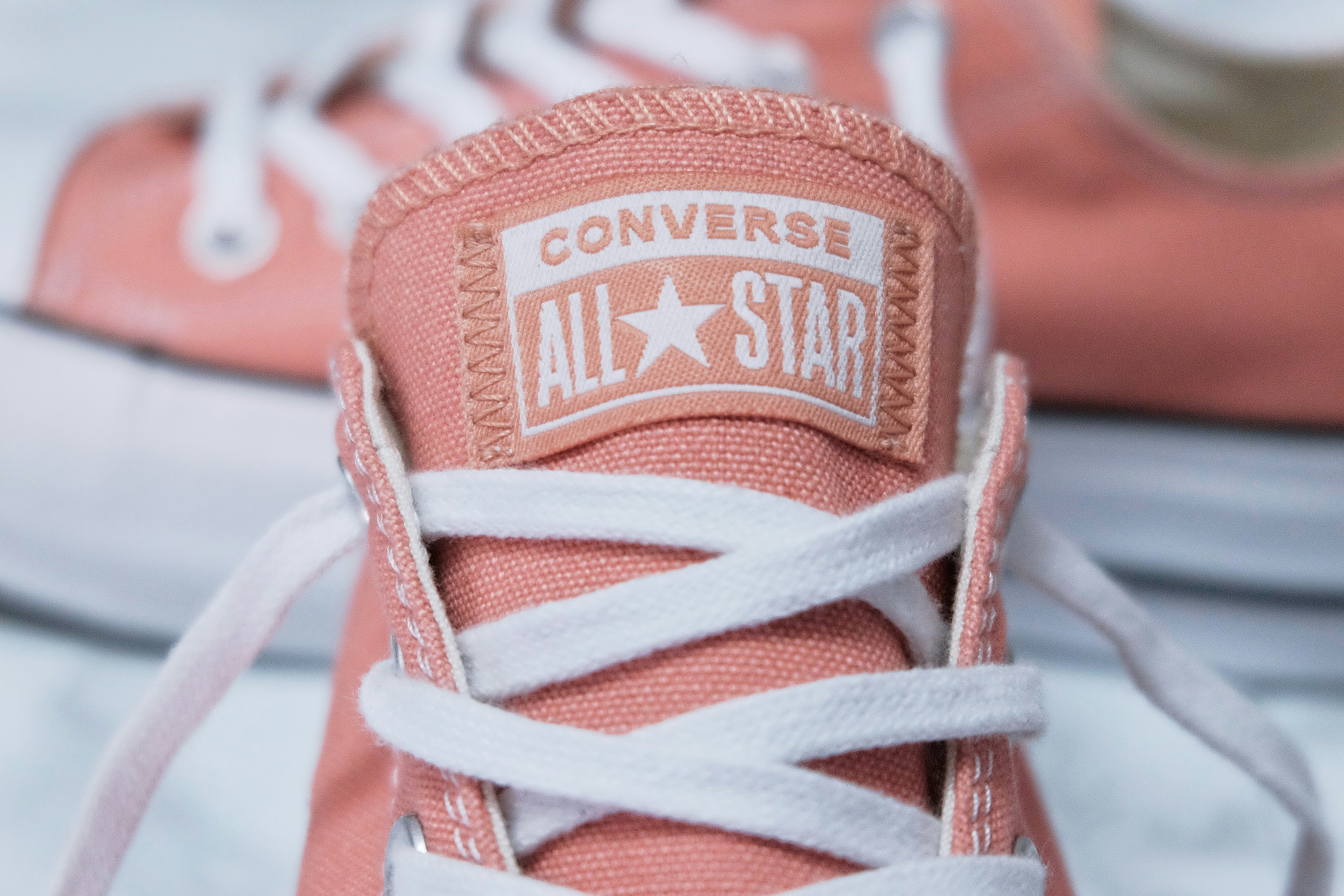 Close-up of a coral Converse All Star sneaker showcasing its iconic logo and laces on a light marble surface.