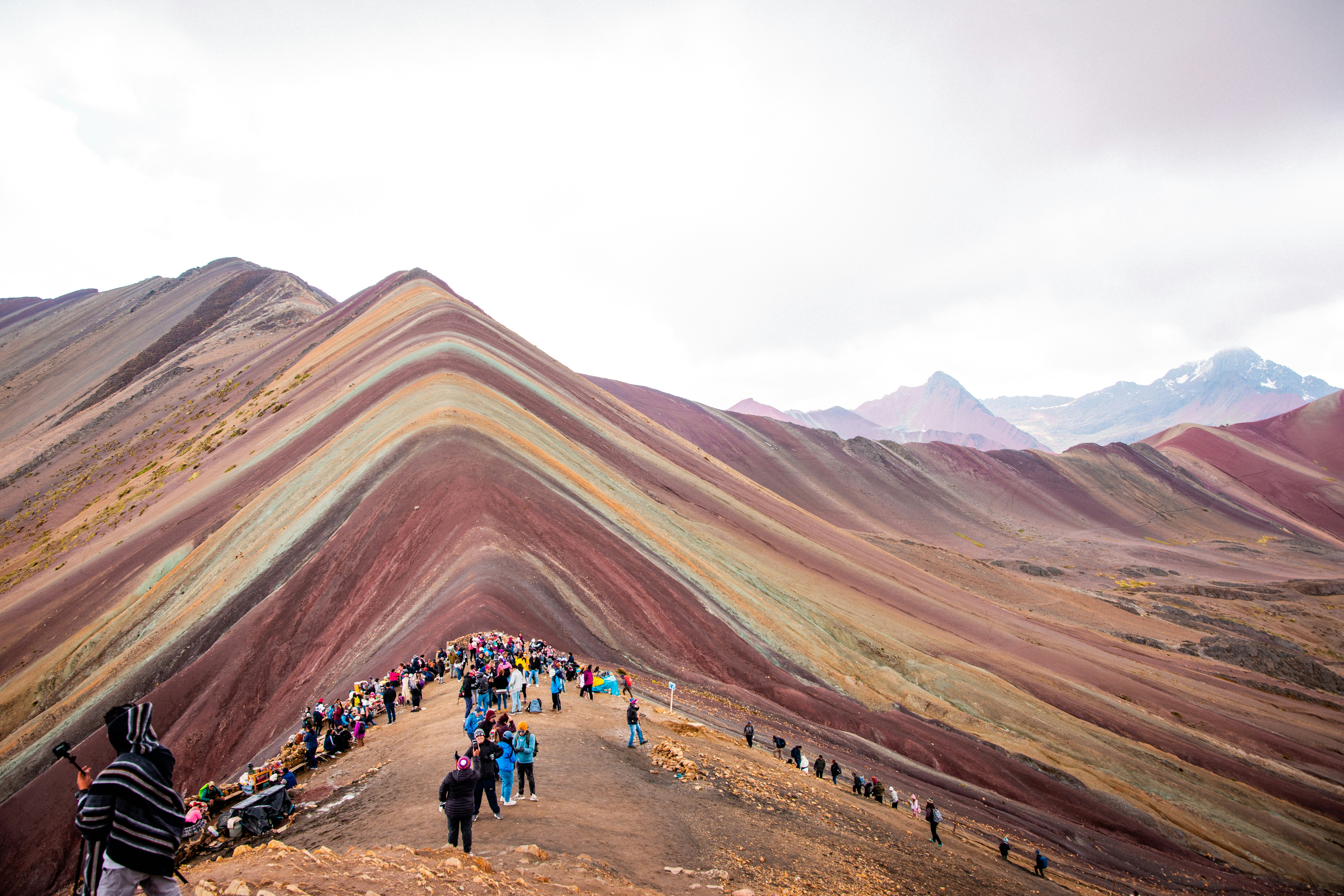 Visitors traverse the colorful slopes of Rainbow Mountain, showcasing the striking geological formations and hues of the landscape. The scene captures the harmony between nature and human exploration.