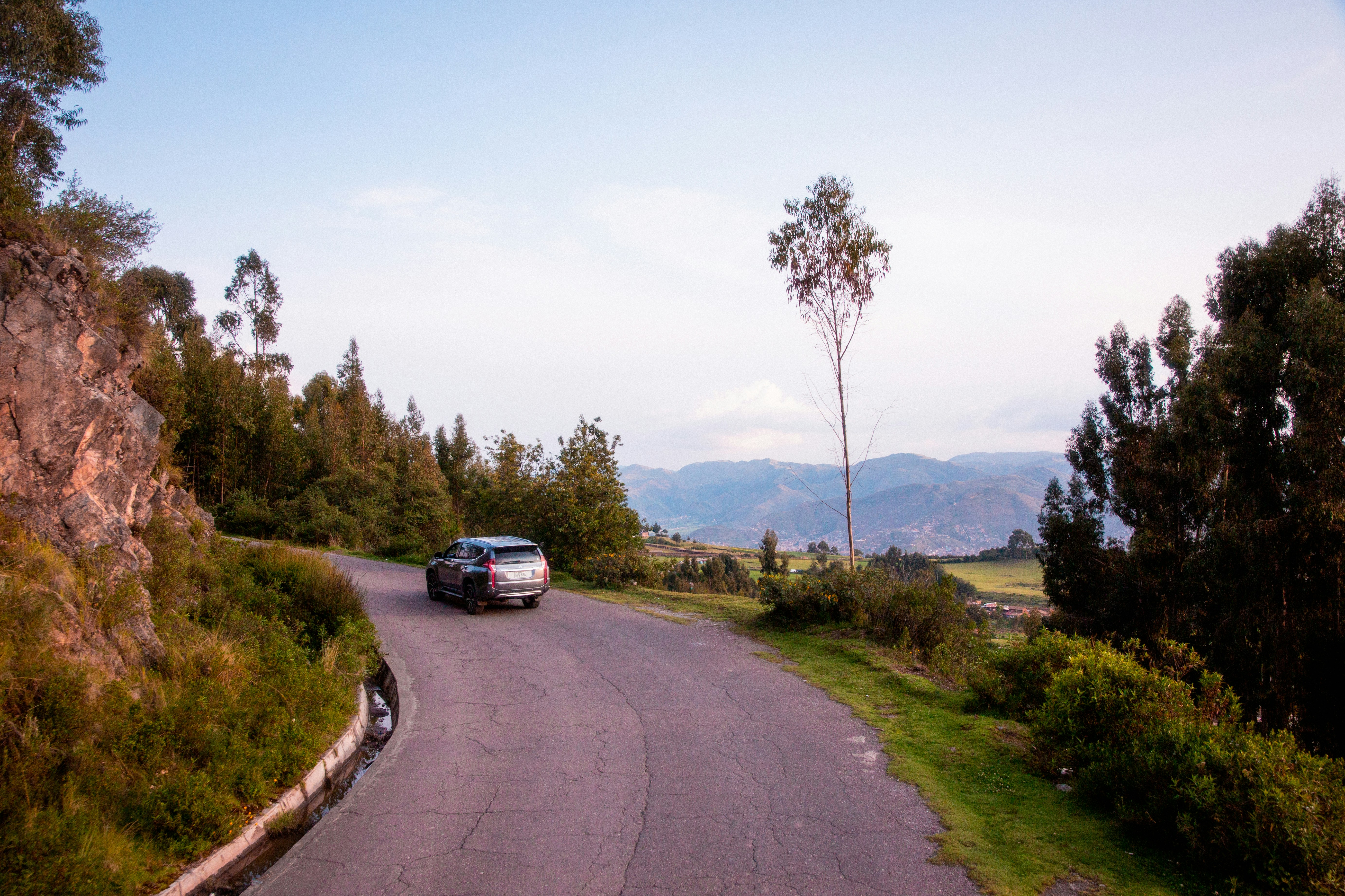 A car navigates a winding road surrounded by lush greenery and distant mountains, showcasing the beauty of a serene landscape.