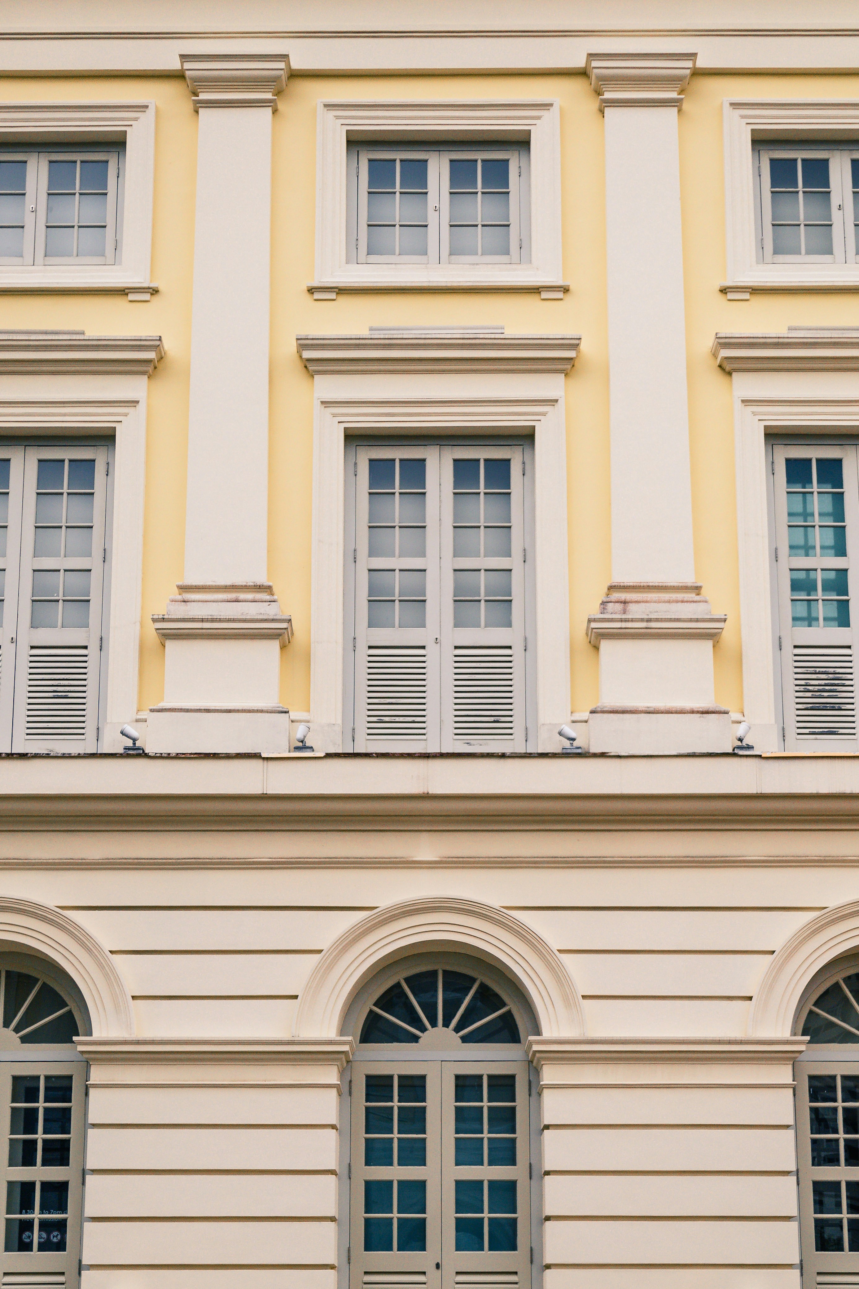 Elegant facade of a building featuring a harmonious arrangement of windows and columns, painted in soft yellow and white tones.