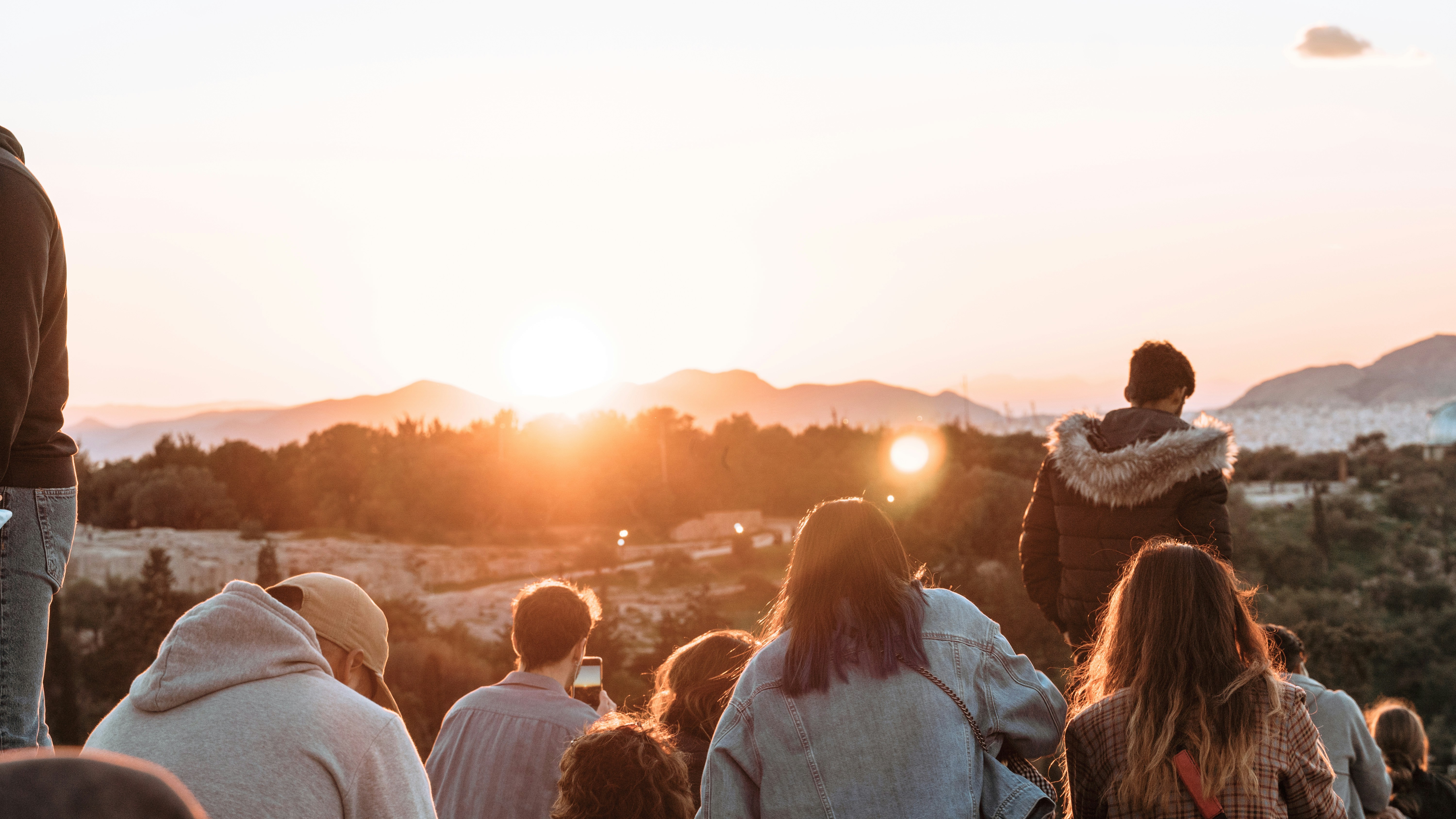 Group of people watching a sunset over distant mountains, creating a serene atmosphere of togetherness.