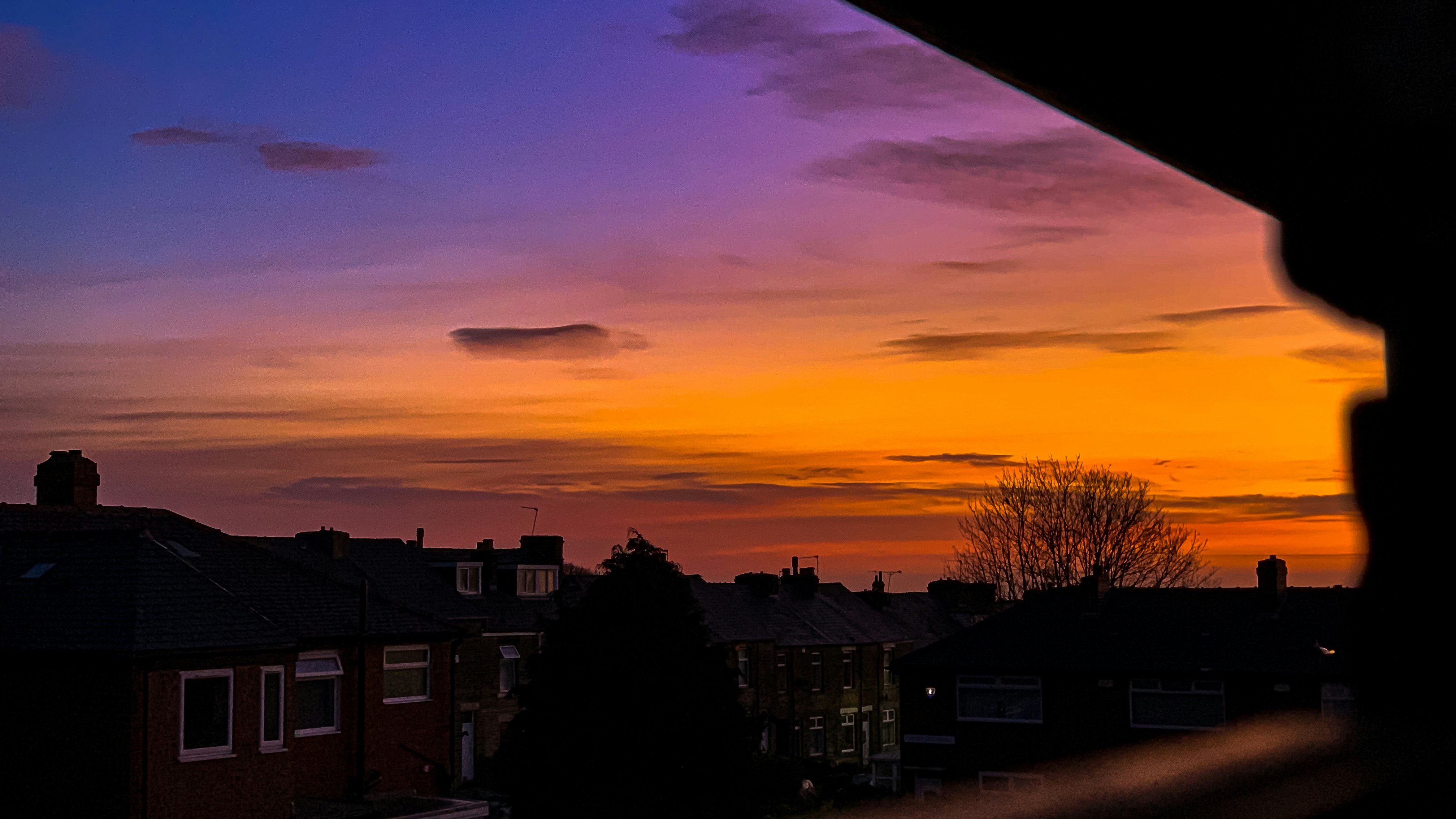 Vibrant sunrise over silhouetted rooftops with deep orange and purple hues.