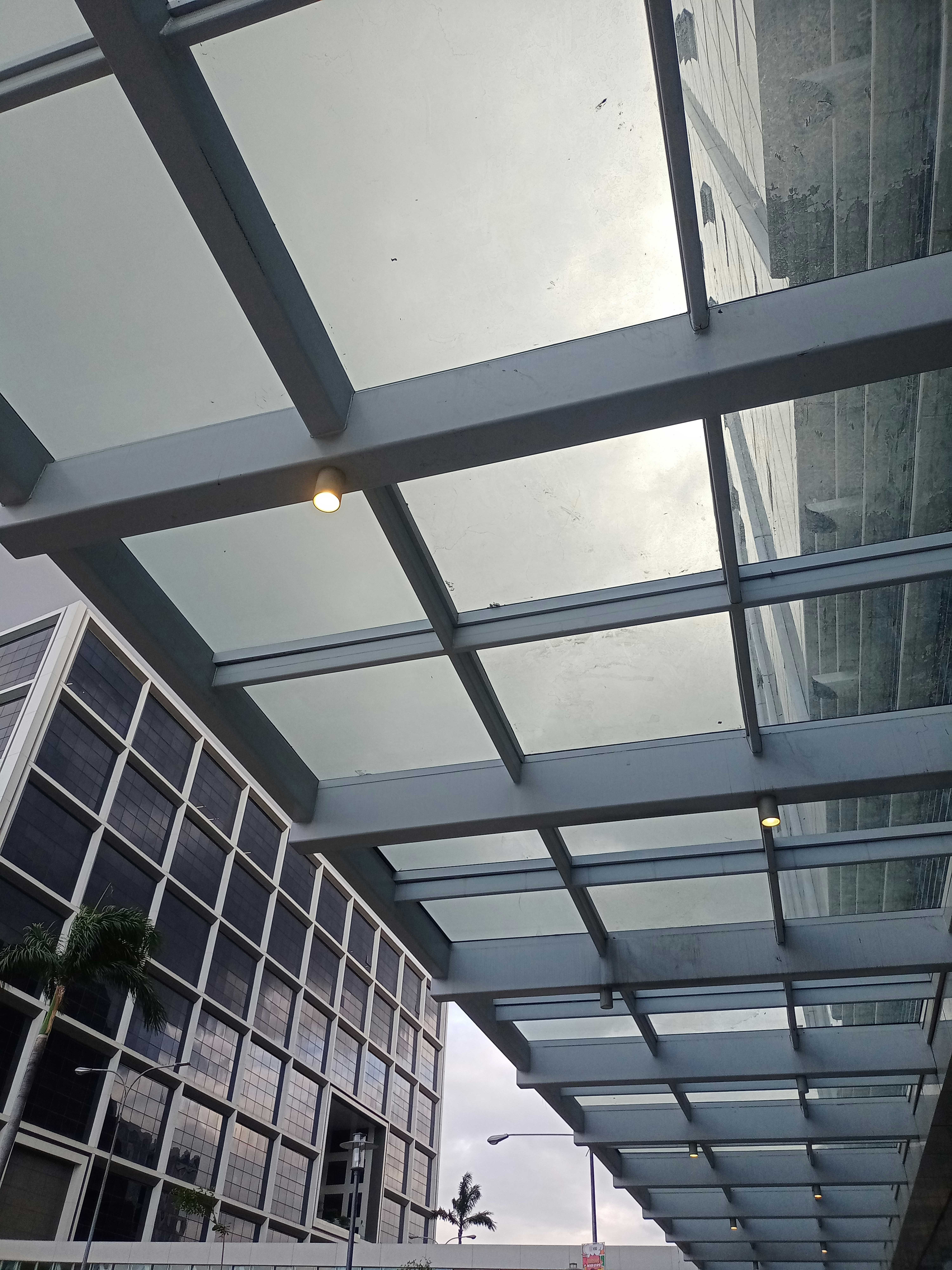 A modern glass canopy frames the sky above, contrasting with the geometric lines of the adjacent buildings. The scene evokes a sense of urban tranquility.