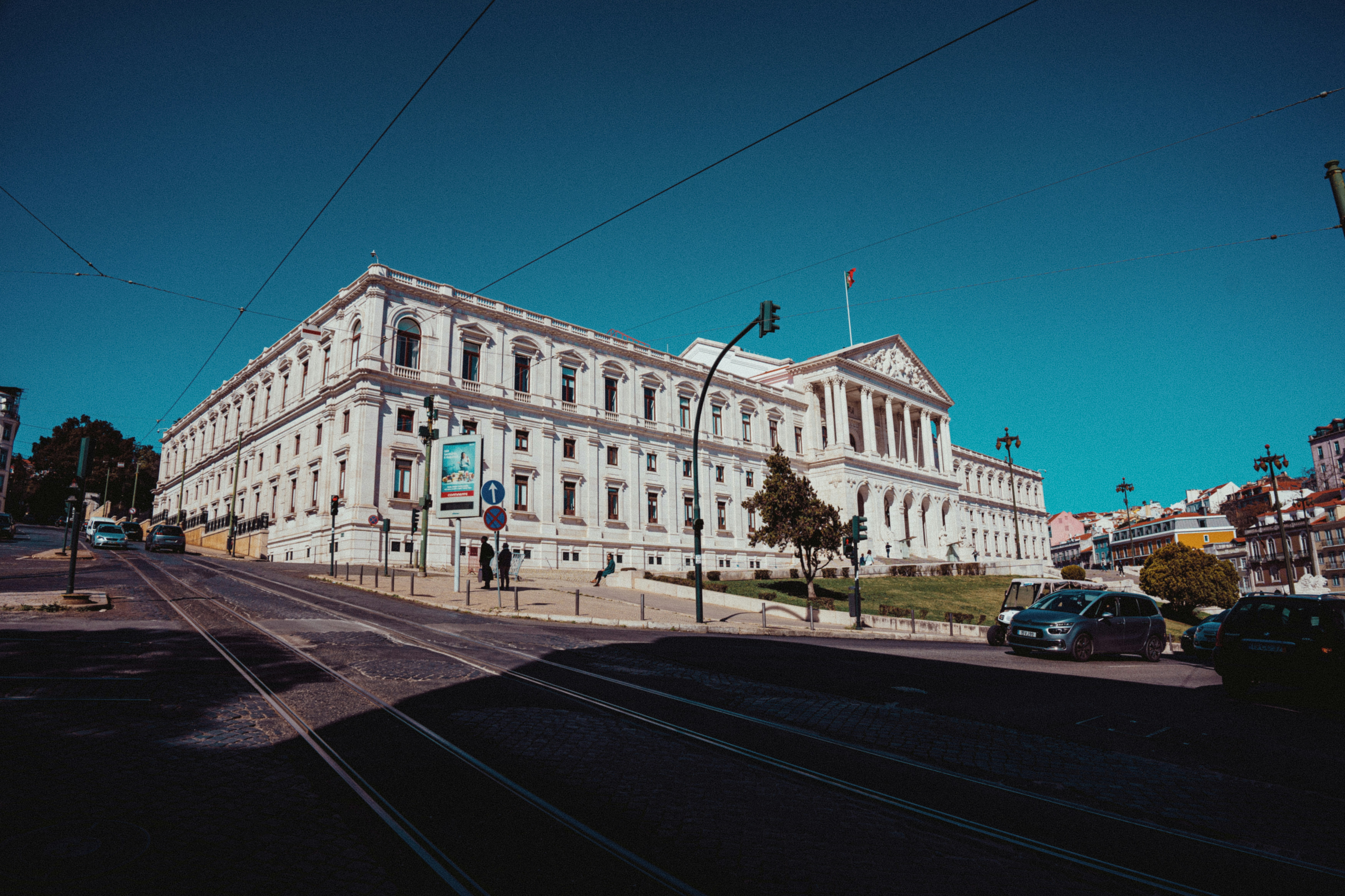 Grand neoclassical government building with a symmetrical facade on a sunlit street in Lisbon.