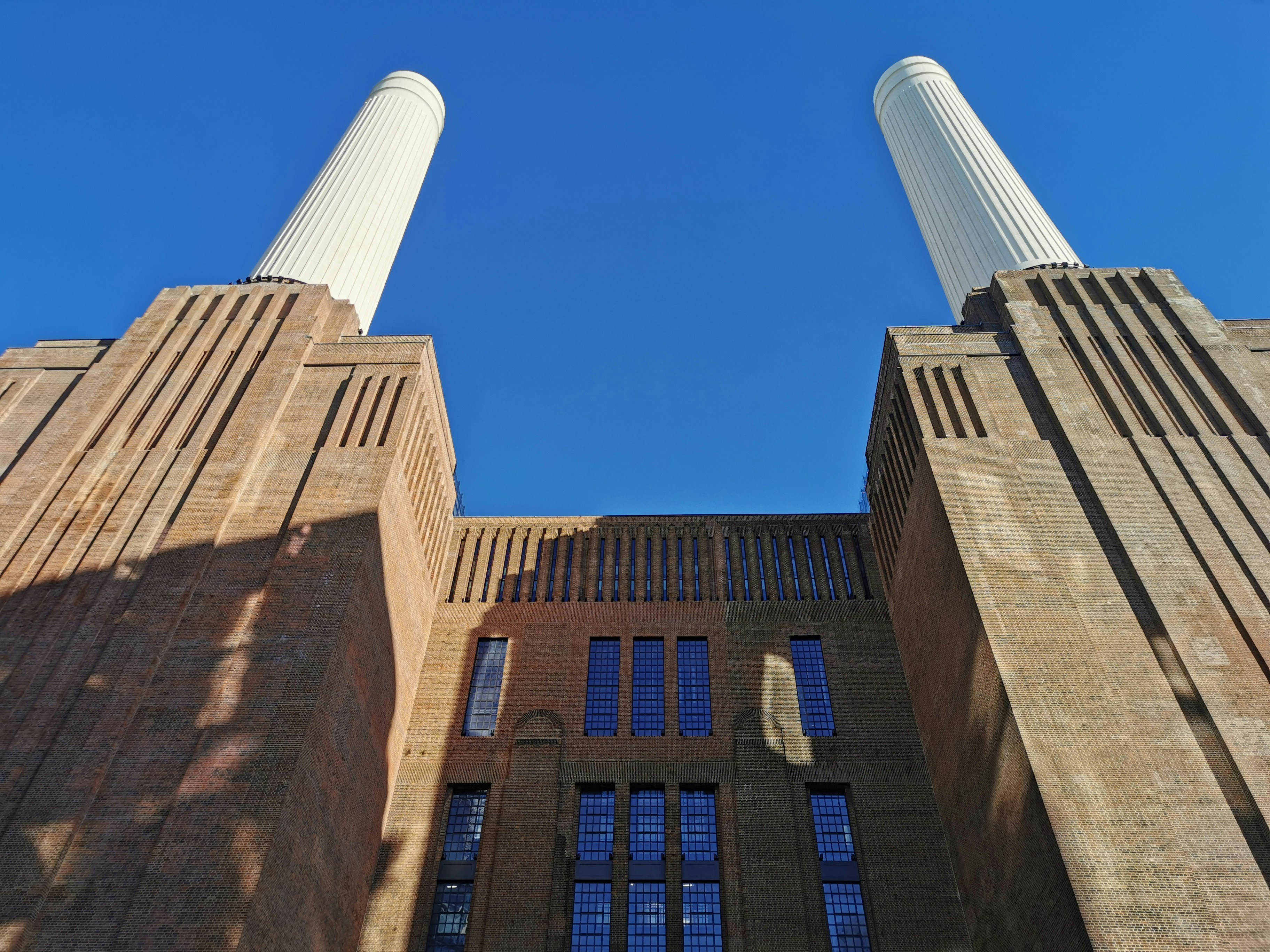 Two towering brick columns flank a central brick facade, seen from a low angle that directs the eye upward toward the clear blue sky. This photograph emphasizes architectural scale and composition, highlighting vertical lines and texture.