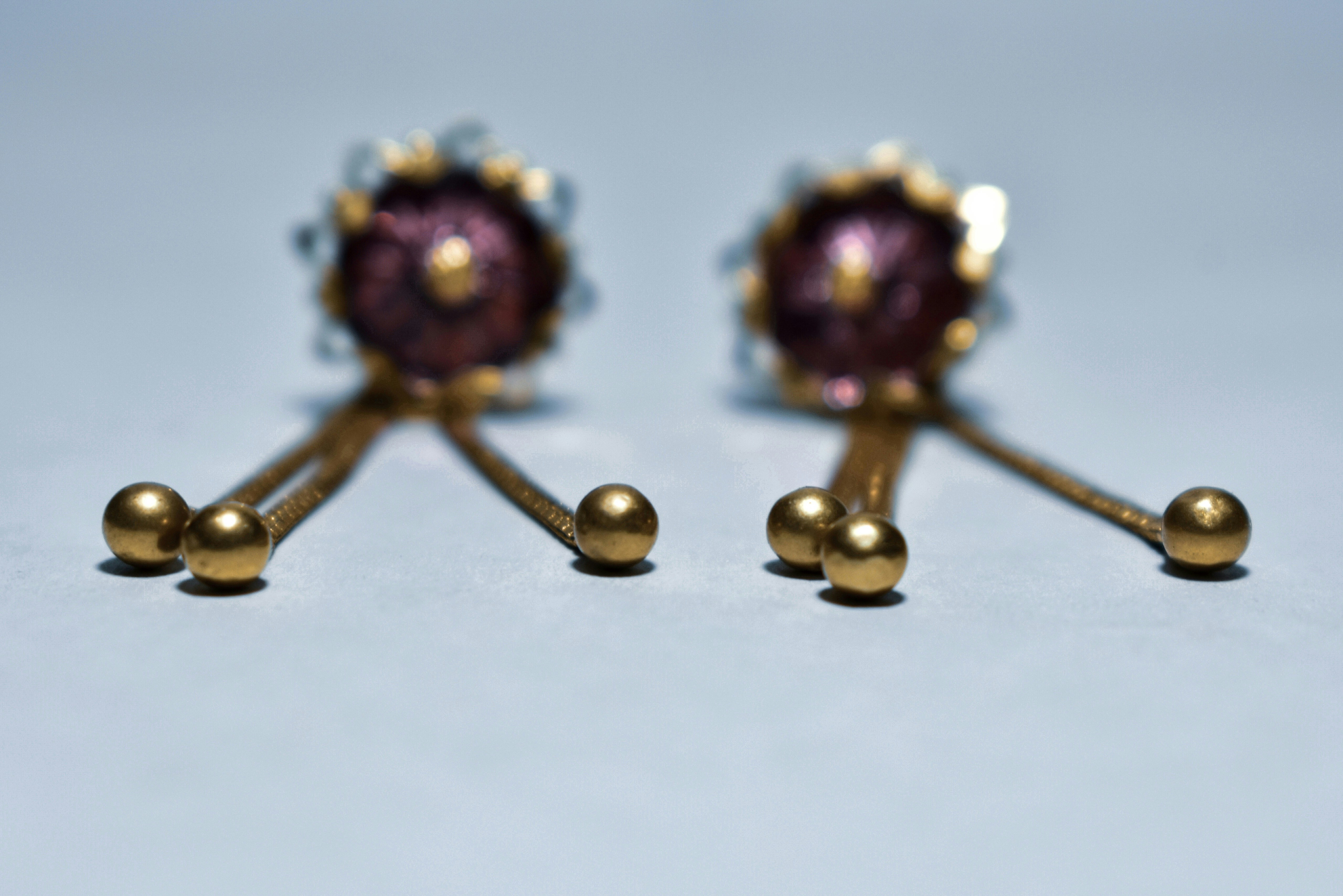 Intricately designed floral hairpins with golden accents and purple centers, resting on a soft blue background.