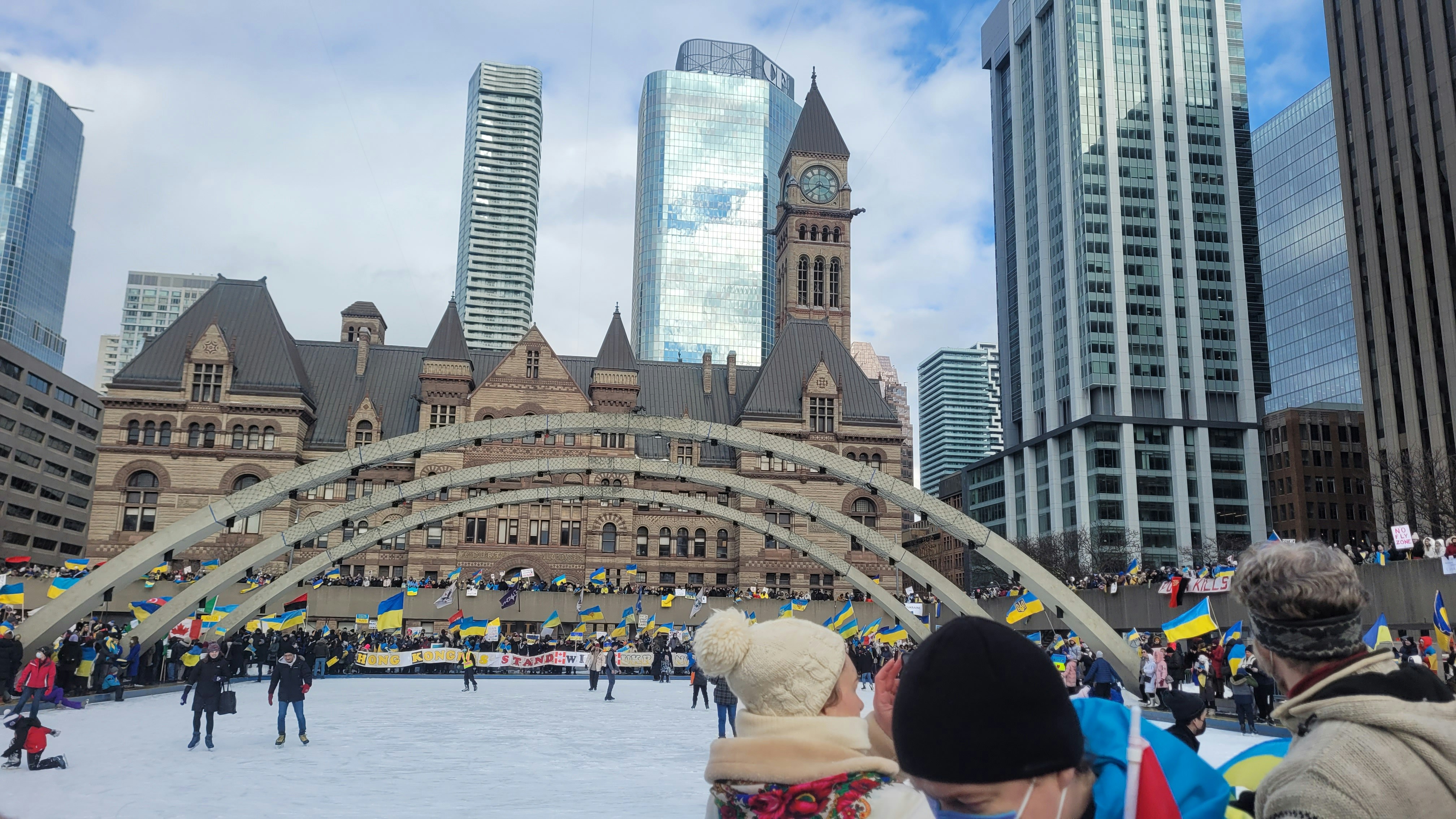 People skating on an ice rink in front of a historic building adorned with colorful flags, showcasing a vibrant community event in an urban setting.